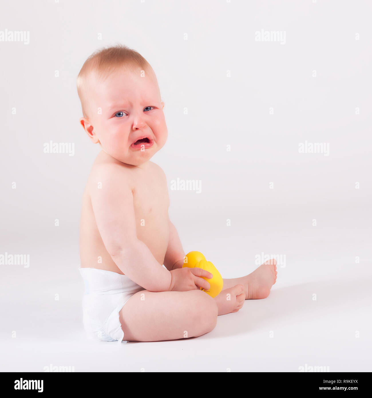 Beautiful nine month crying baby in diaper sitting on the ground ...