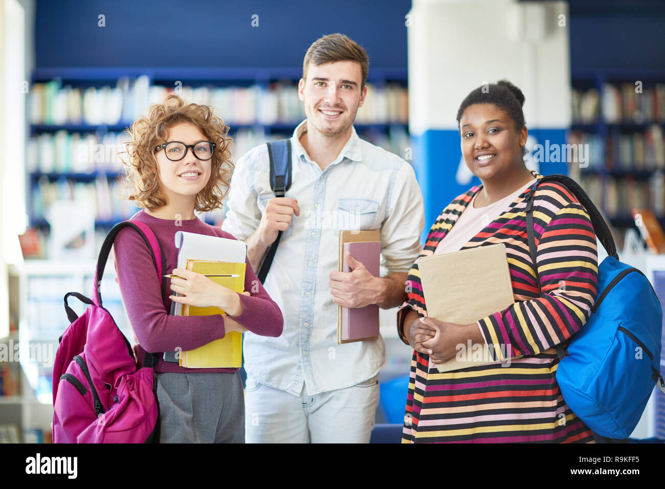 Happy students with books in library Stock Photo - Alamy