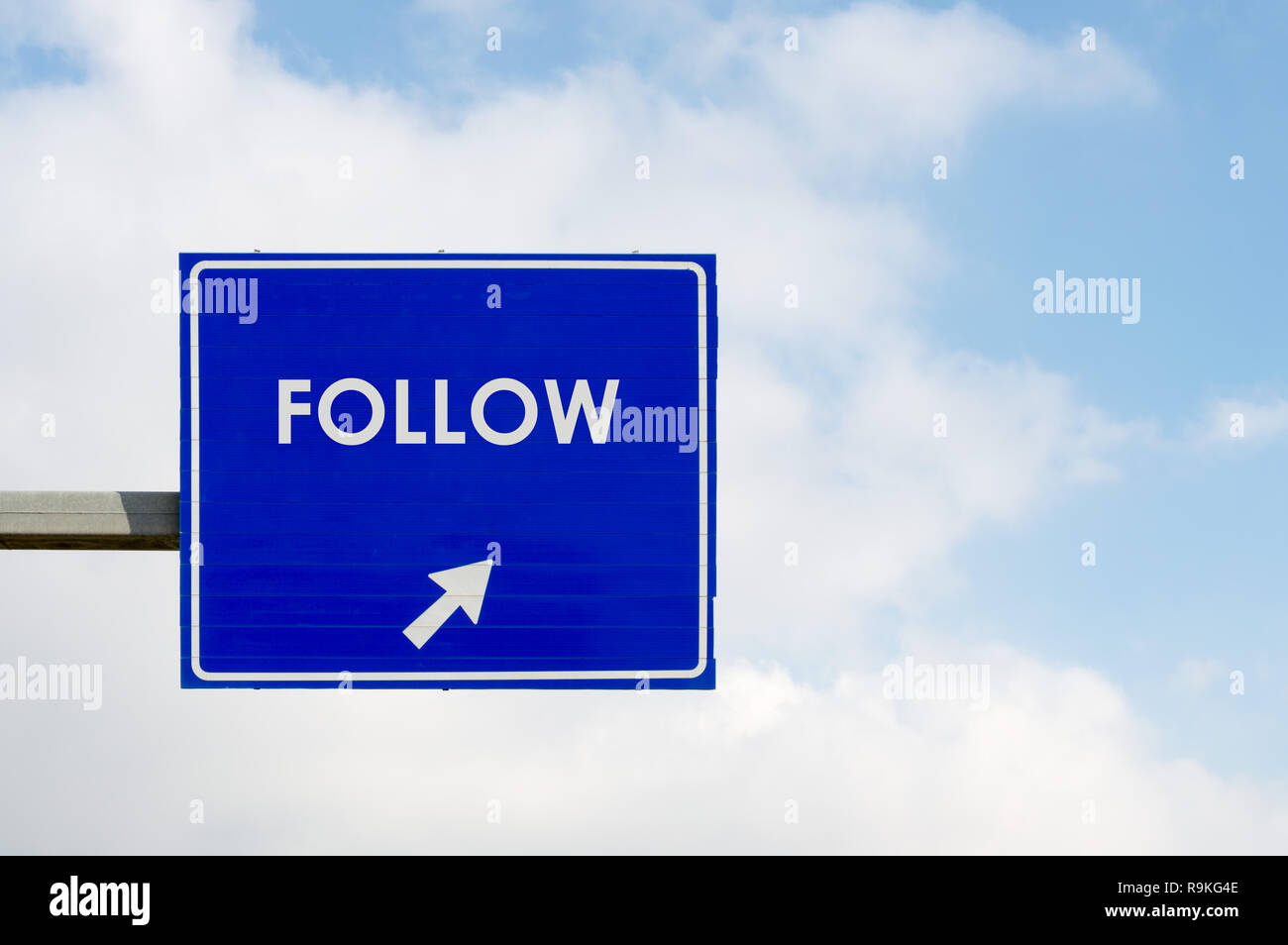 Blue road sign displaying Follow word on blue sky and white clouds ...