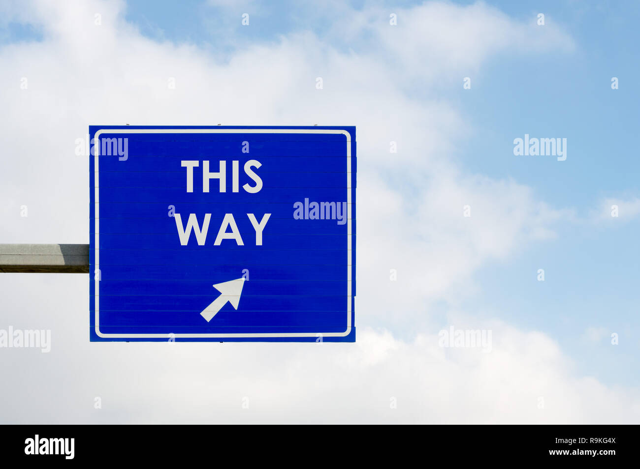 Blue road sign displaying This Way words on blue sky and white clouds ...