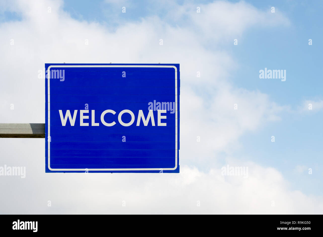 Blue road sign displaying Welcome word on blue sky and white clouds ...