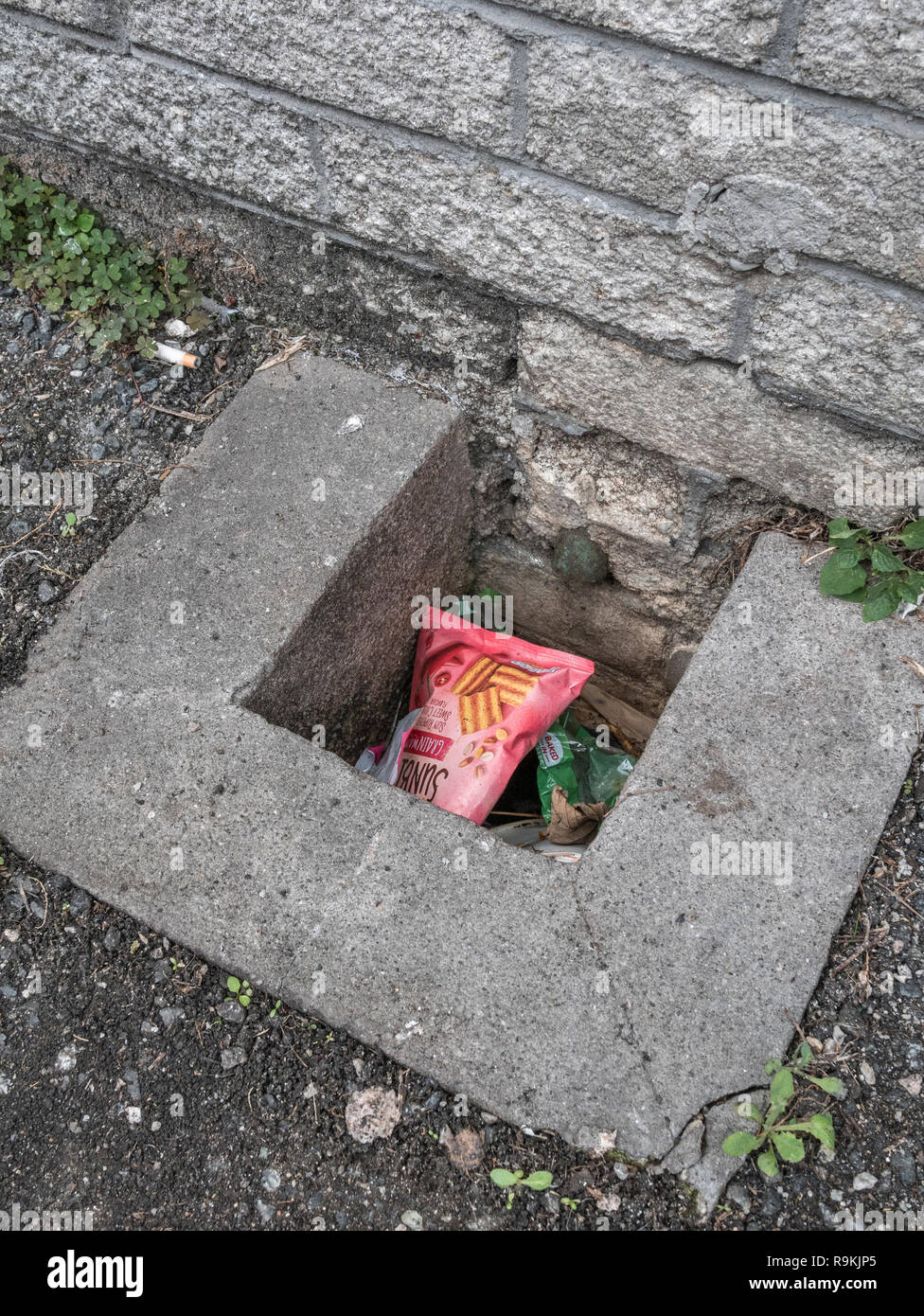 Plastic food wrapper discarded in urban drain. Metaphor plastic ...