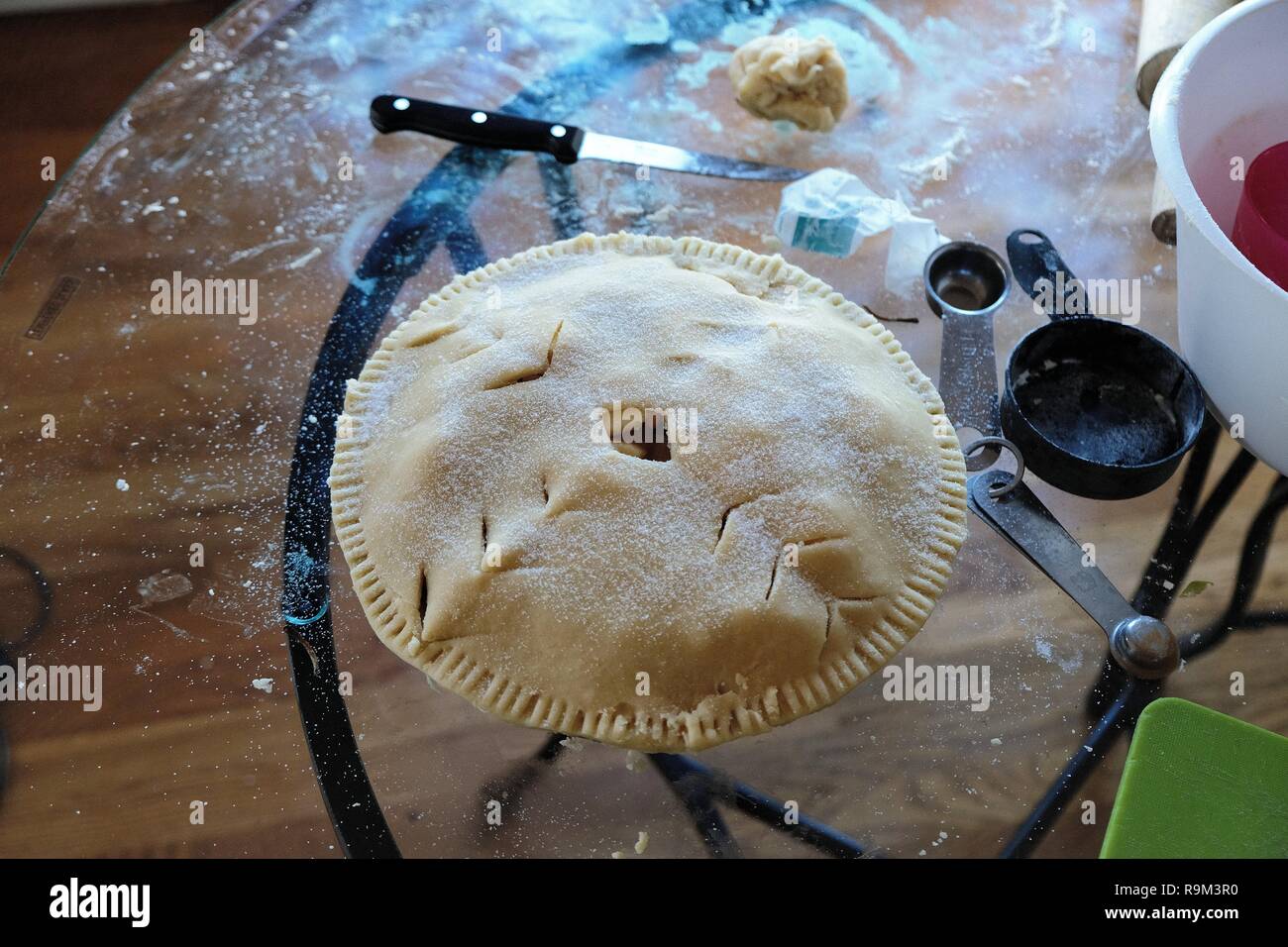 Unbaked apple pie on messy glass table surrounded by measuring spoons ...