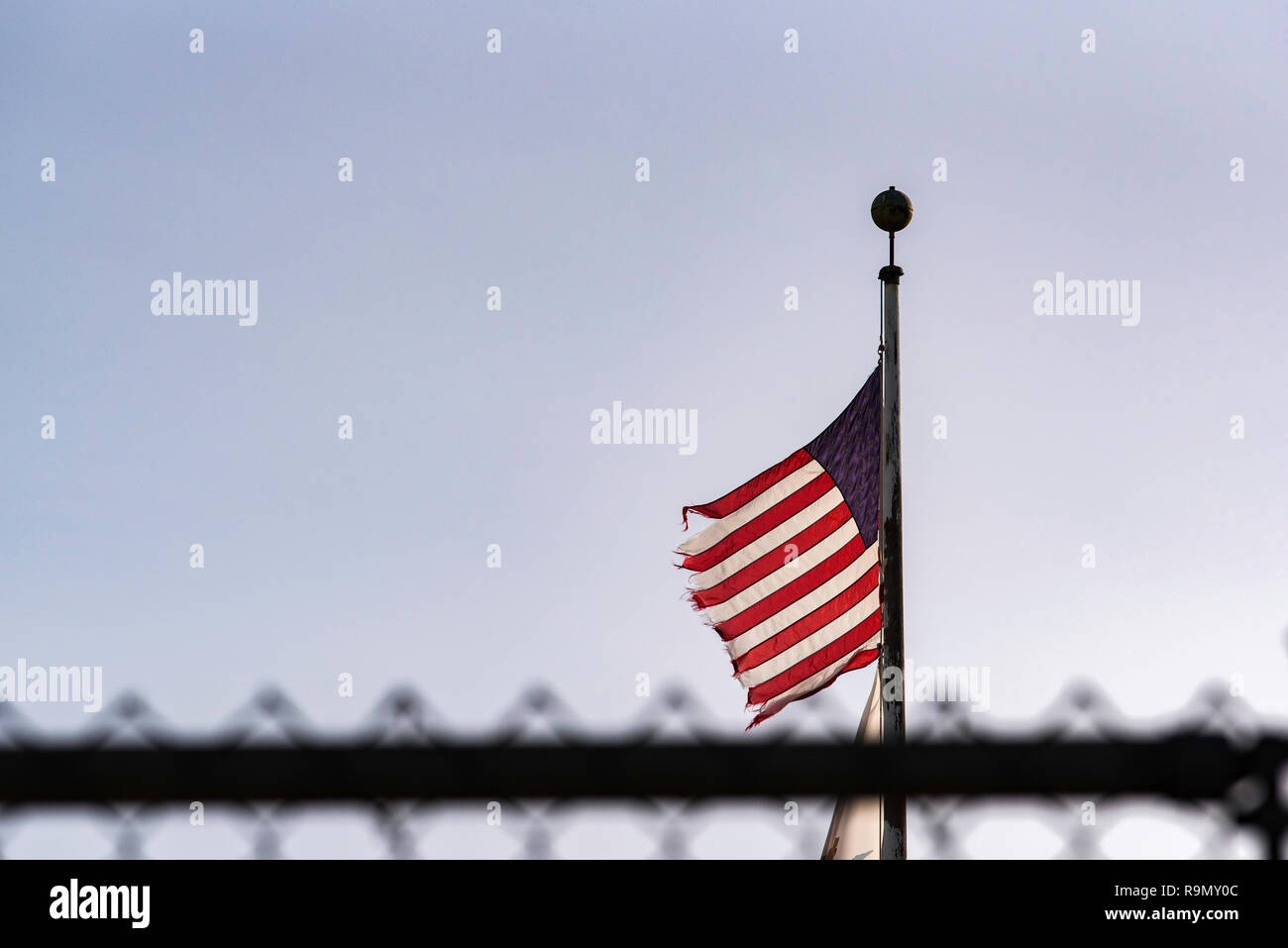 A frayed and worn American (USA) flag flies above a wire fence Stock ...
