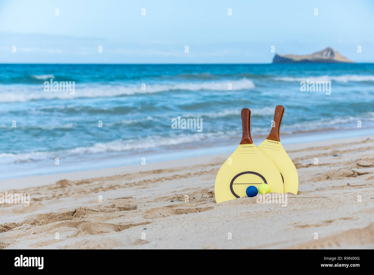 Yellow beach paddle and balls on a sandy beach in Hawaii with waves and ...