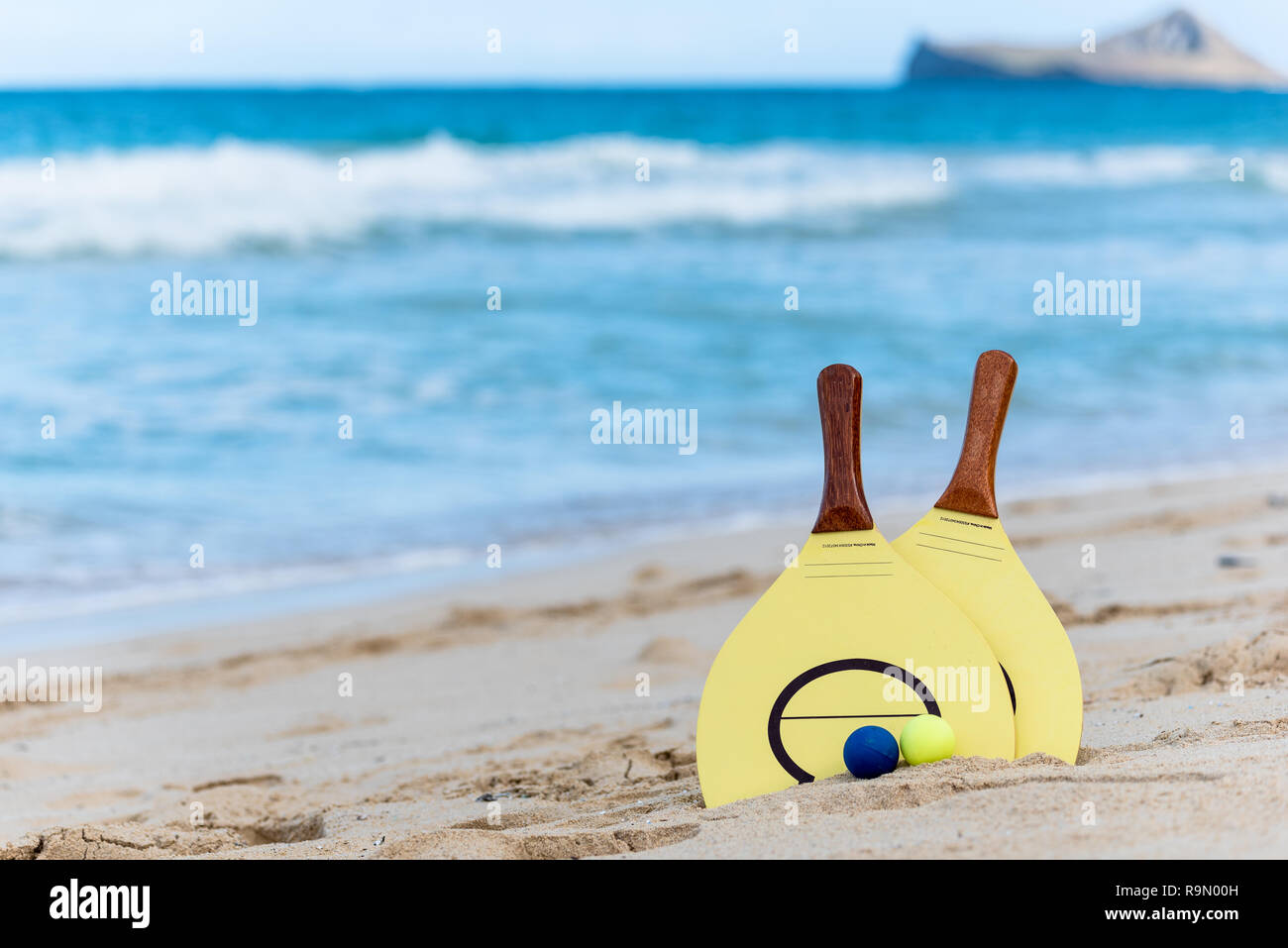 Yellow beach paddle and balls on a sandy beach in Hawaii with waves and ...