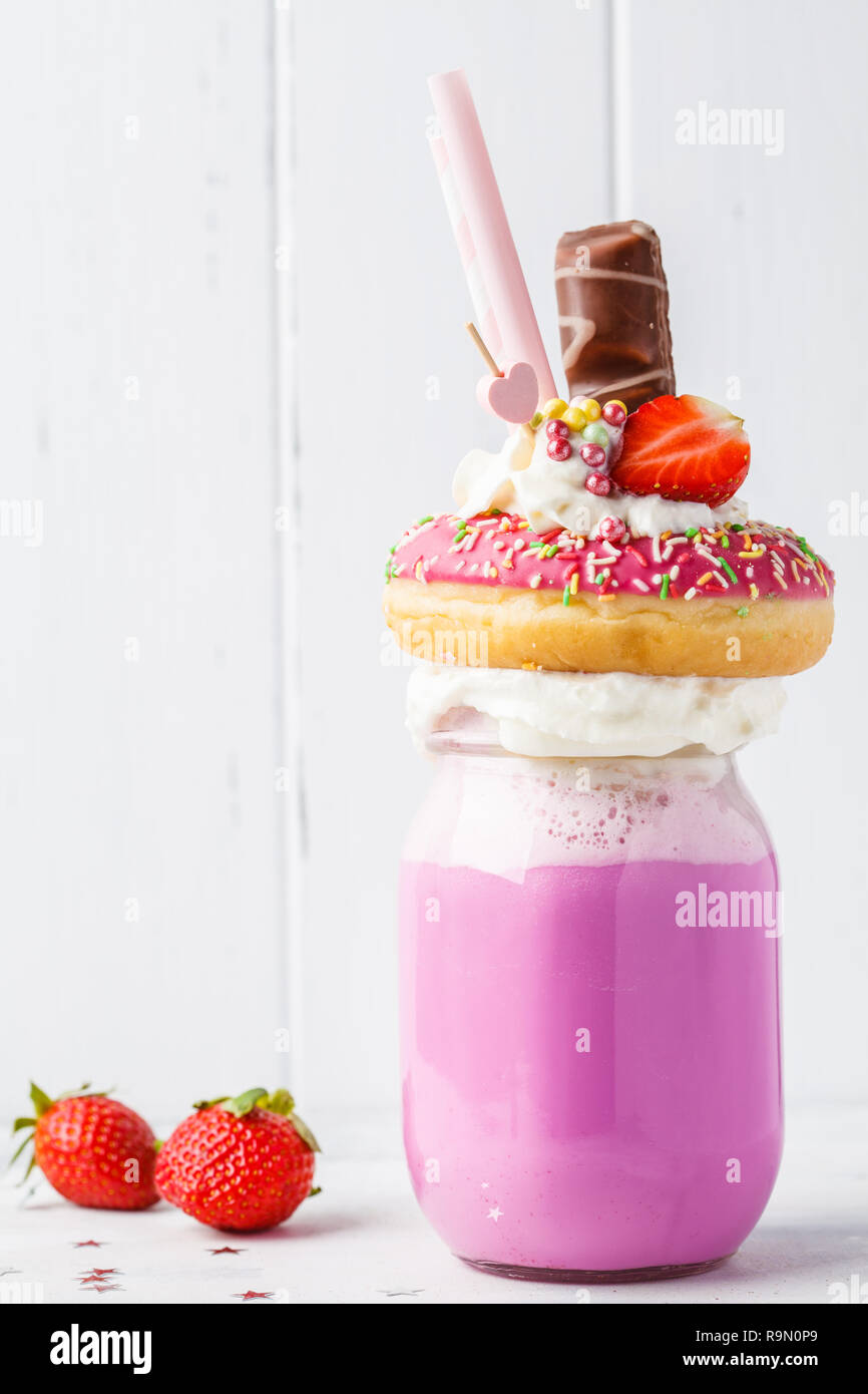 Pink strawberry Freak Shake cocktail with donut and sweets on a white ...