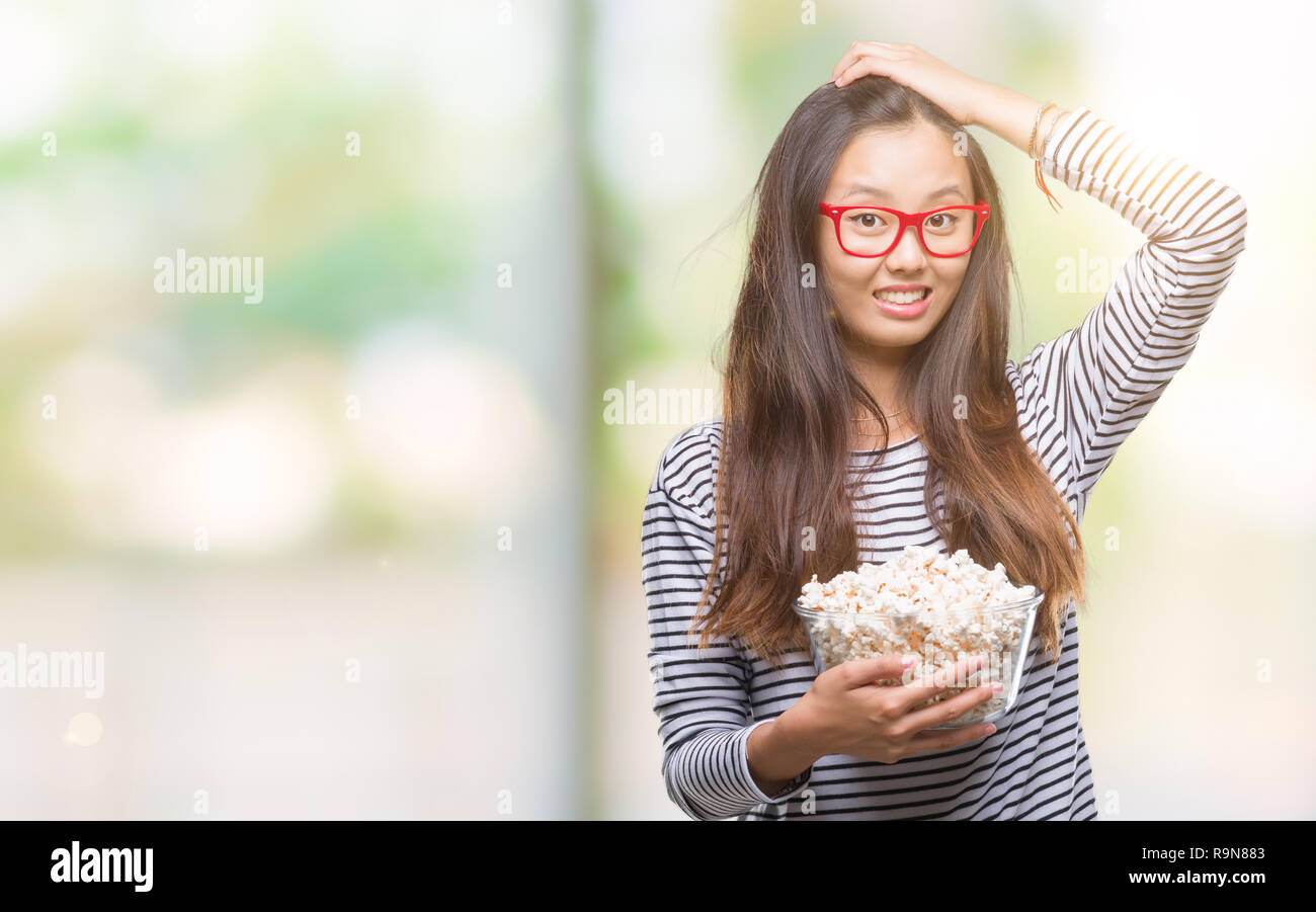 Young asian woman eating popcorn over isolated background stressed with ...