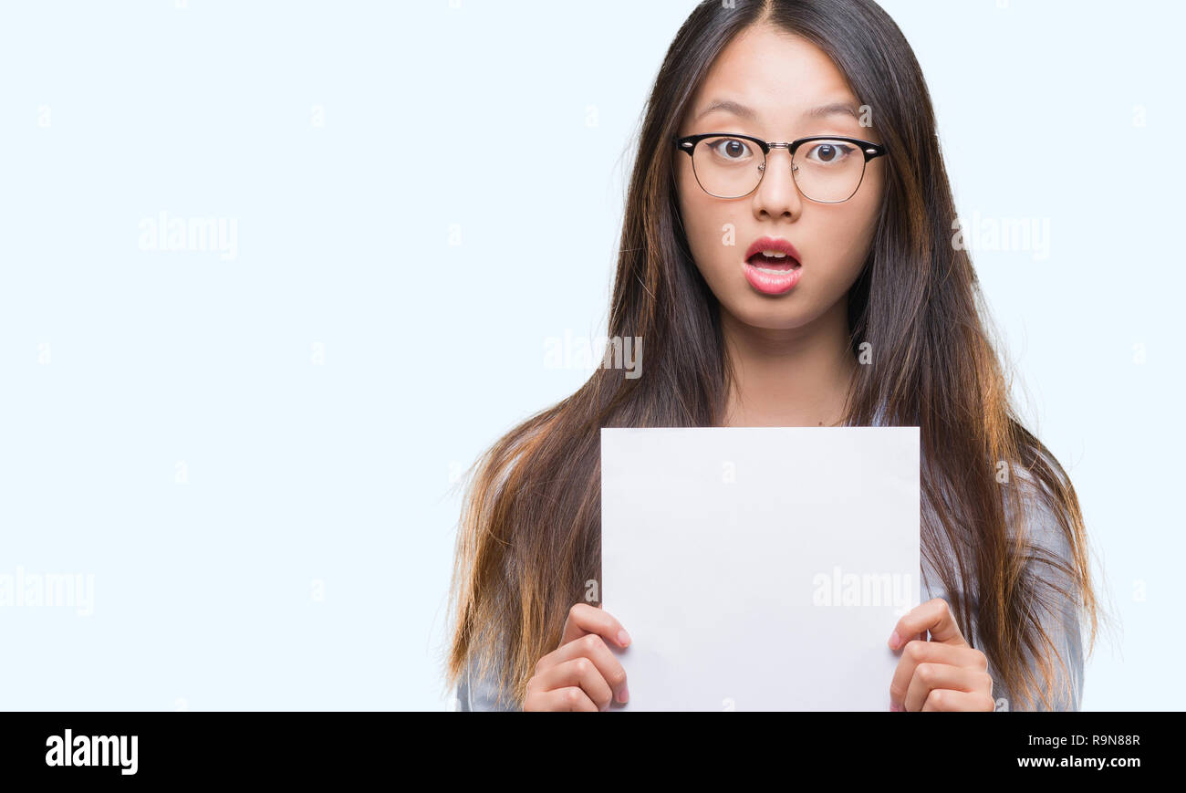 Young asian woman holding blank paper over isolated background scared ...