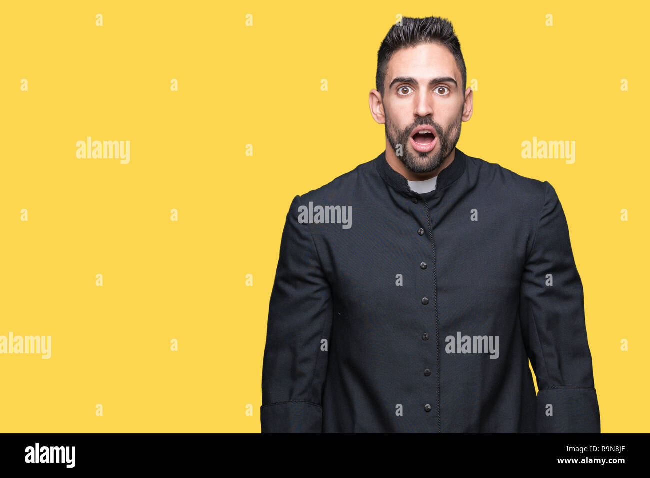 Young Christian priest over isolated background afraid and shocked with ...