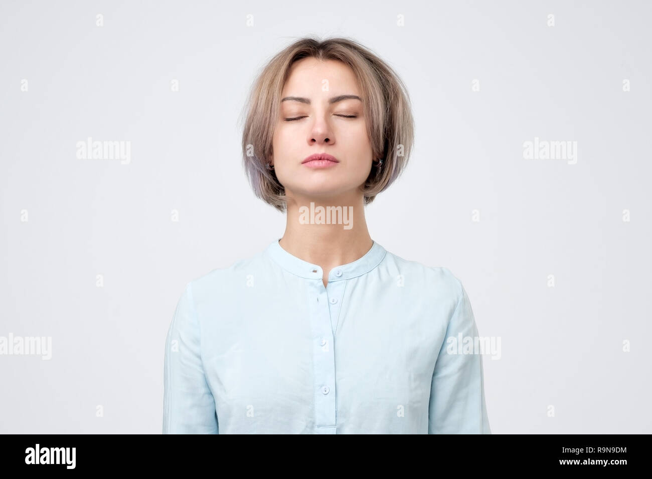 Young european woman in blue shirt closing eyes. No emotion on her face ...