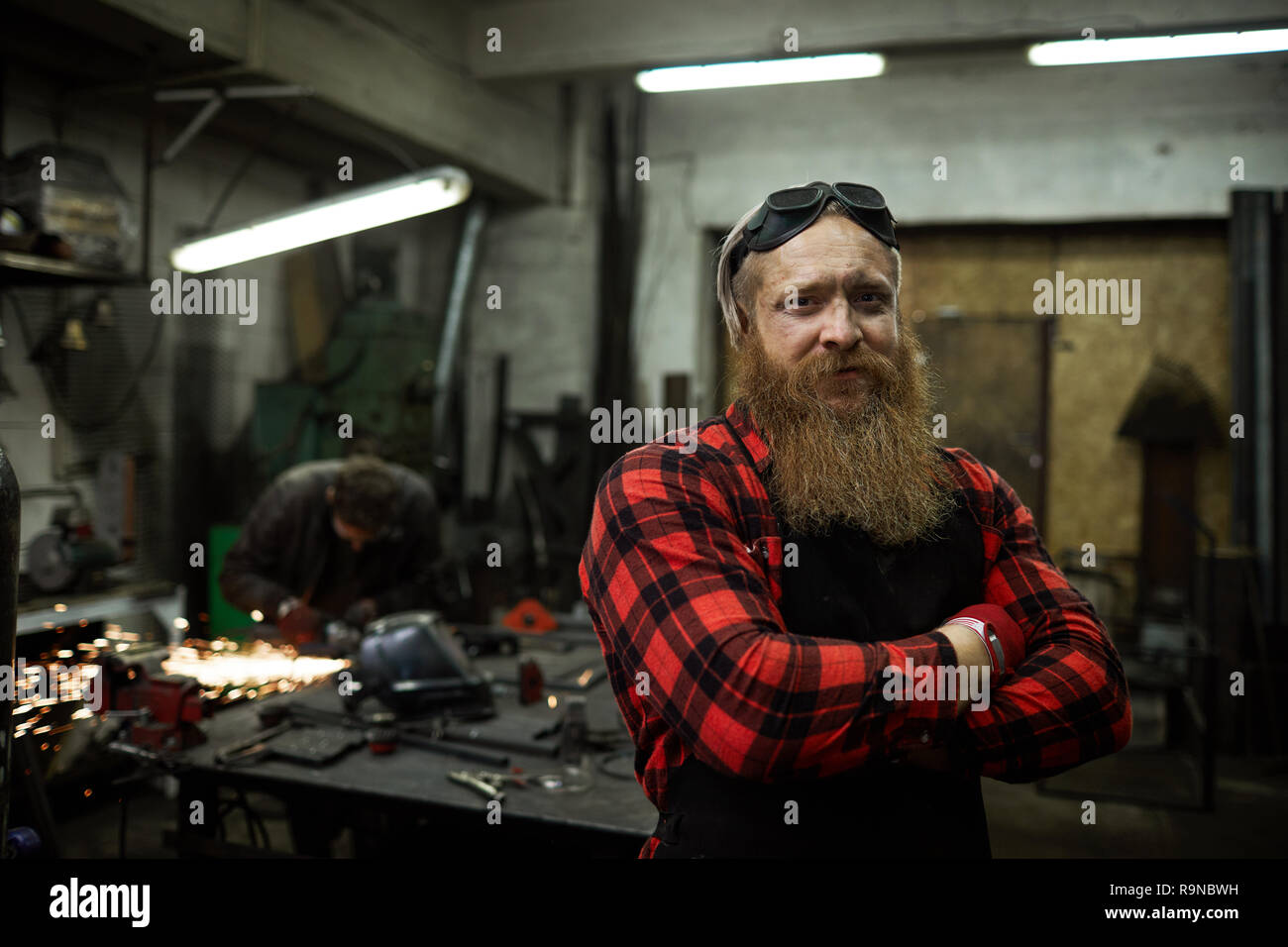 Content blacksmith in safety goggles on head in welding shop Stock ...