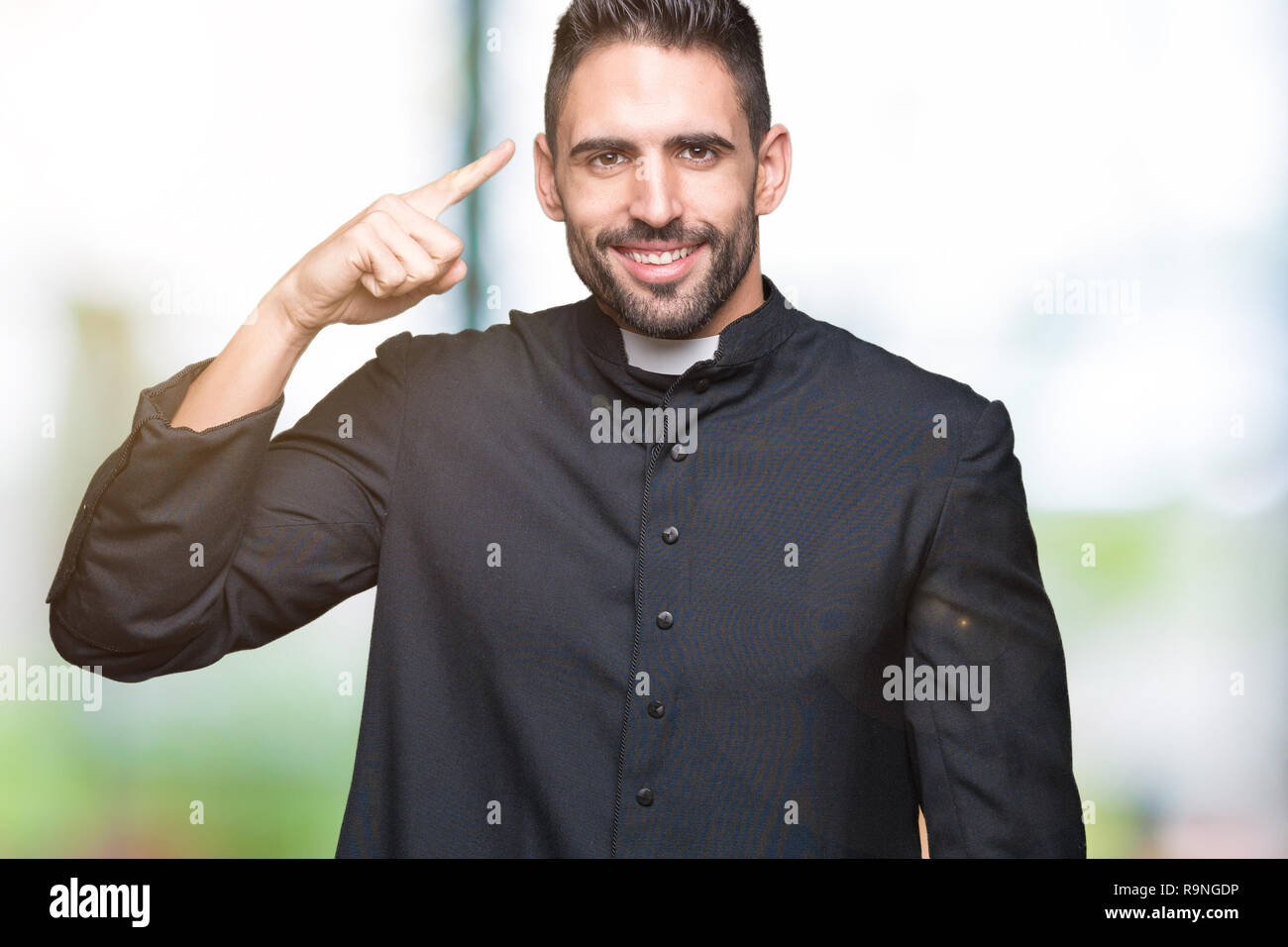 Young Christian priest over isolated background Smiling pointing to ...