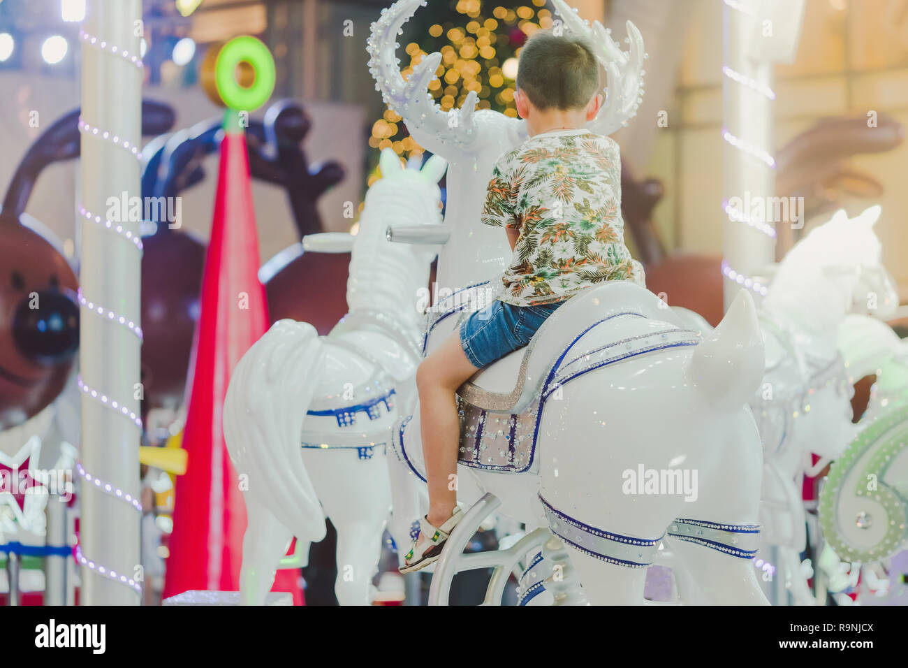 Adorable Asian little kid boy riding on a merry go round carousel ...