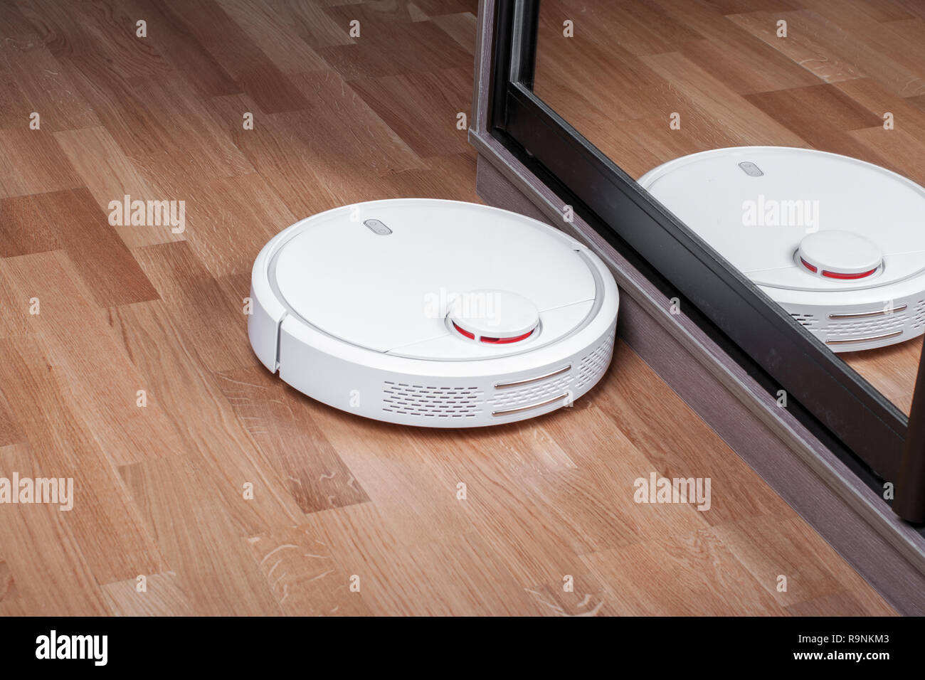 Robotic vacuum cleaner on laminate floor is reflected in mirror of ...