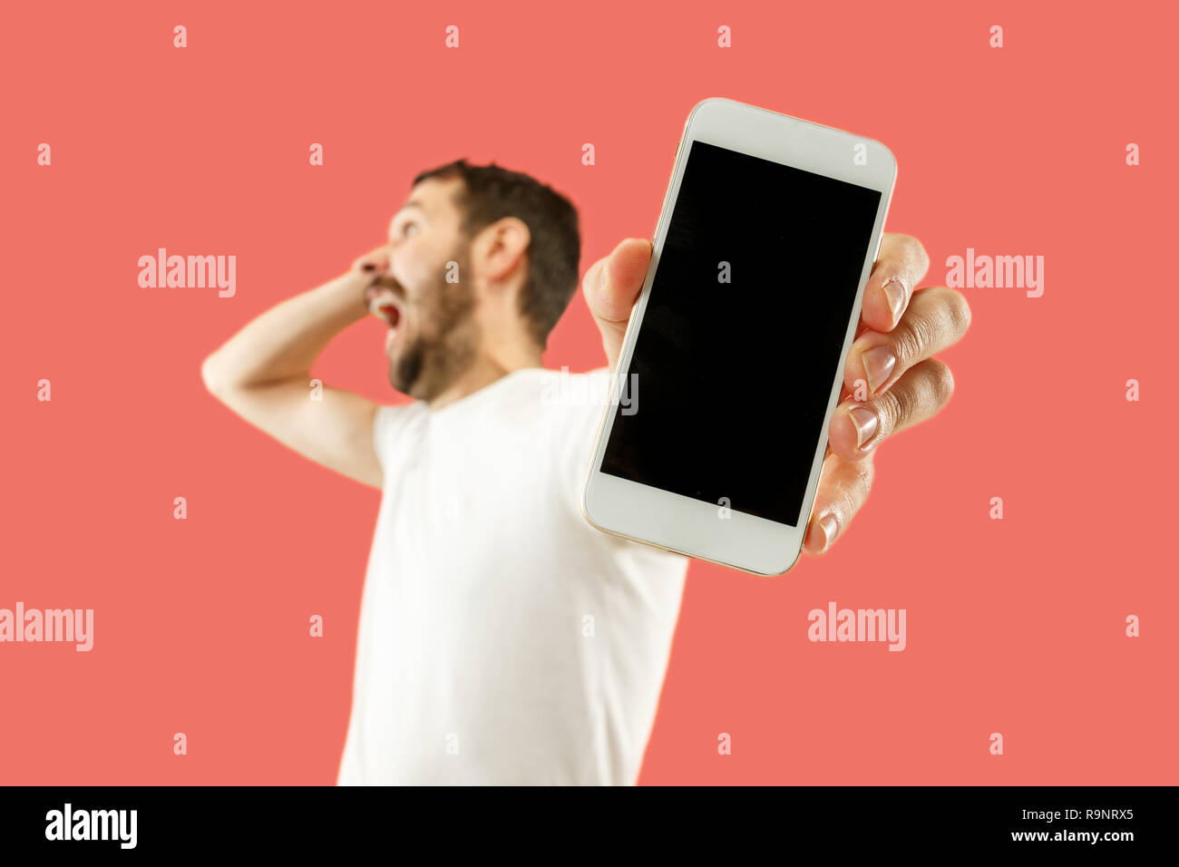 Young handsome man showing smartphone screen over coral background with ...