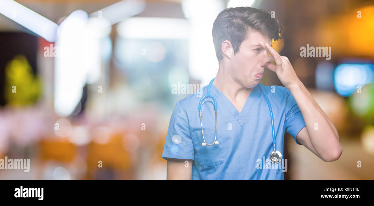 Young doctor wearing medical uniform over isolated background smelling ...