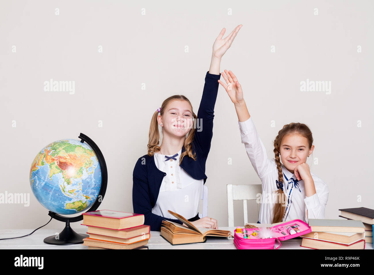 two schoolgirls girls in class at her desk with books hand to answer ...