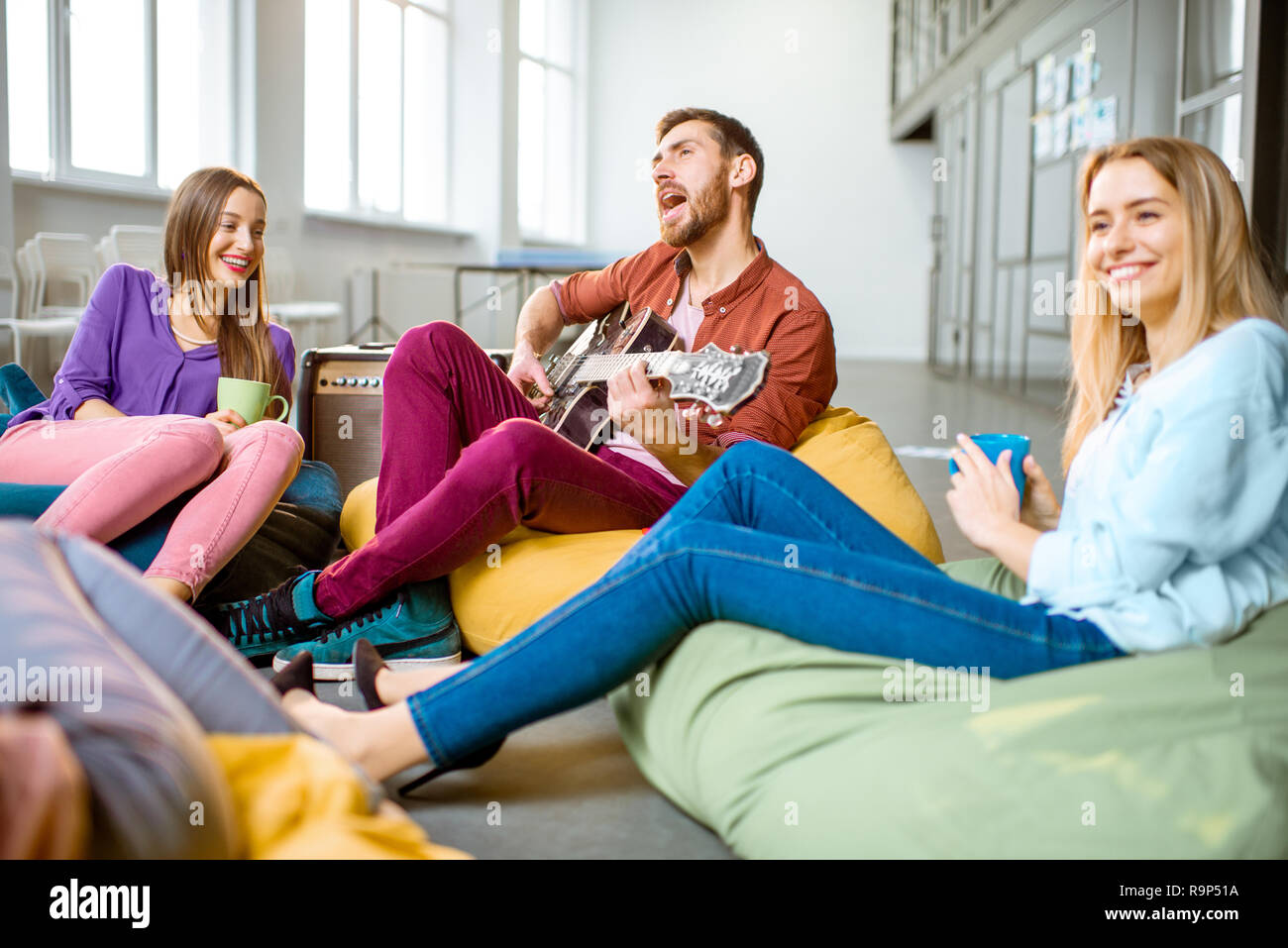 Group of a young coworkers having fun sitting on the colorful poufs ...