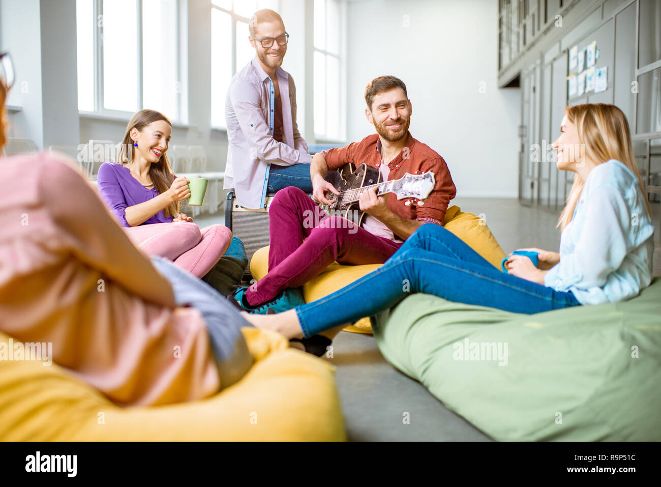 Group of a young coworkers having fun sitting on the colorful poufs ...