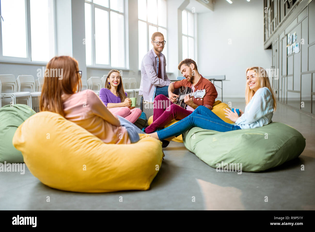 Group of a young coworkers having fun sitting on the colorful poufs ...