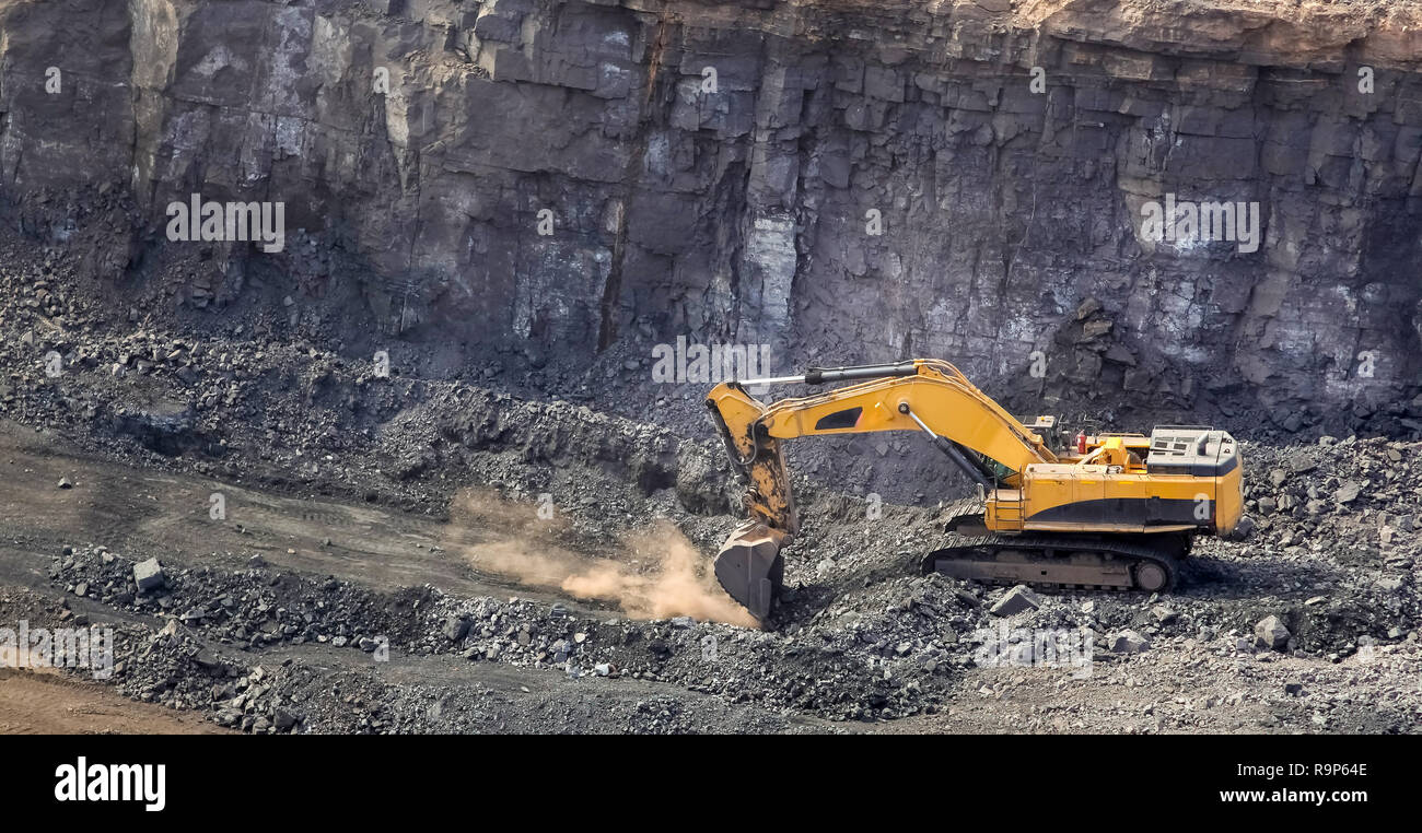 Yellow excavator digging for ore rich rock in an open pit mine Stock ...
