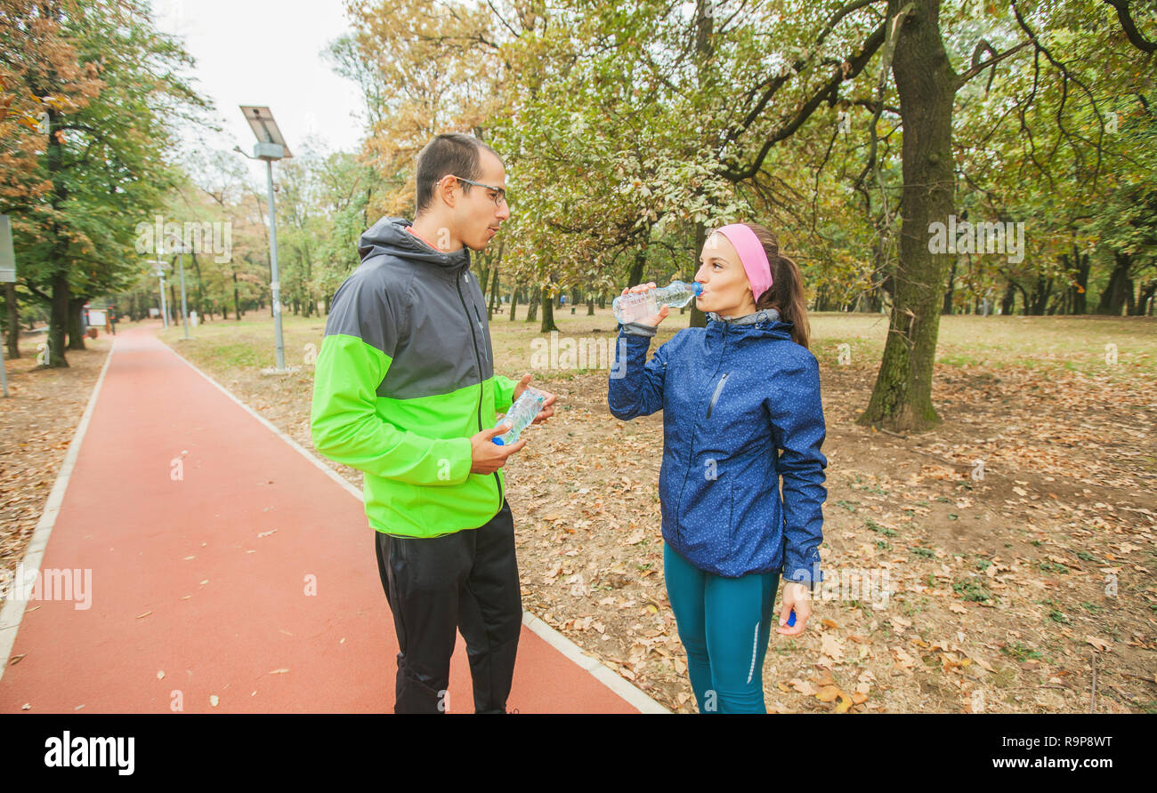 Happy young couple relaxing on fitness trail and refreshing with water ...
