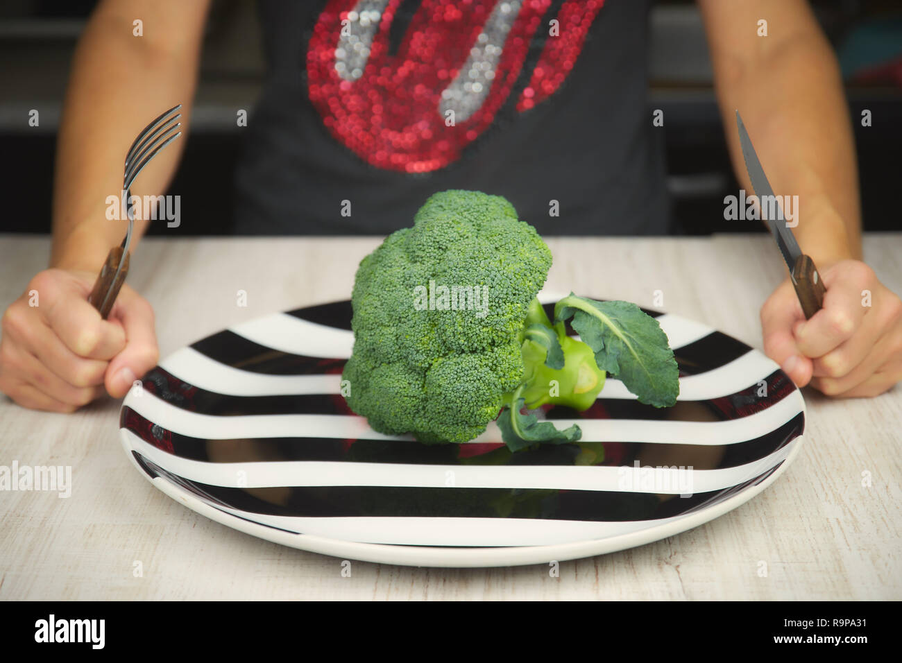 The concept of raw food. Woman eating at the table green raw broccoli ...