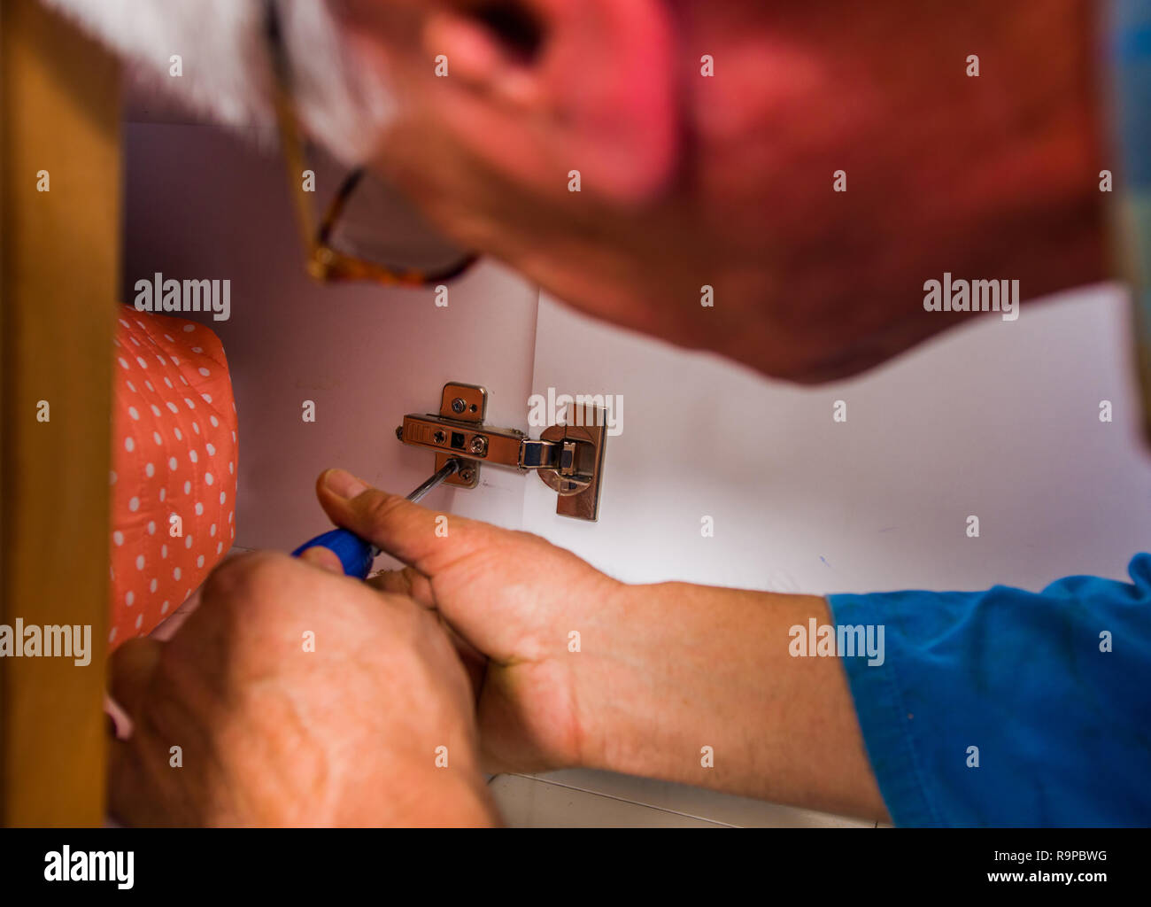 Old age handyman in working suit is fixing the cupboard with ...