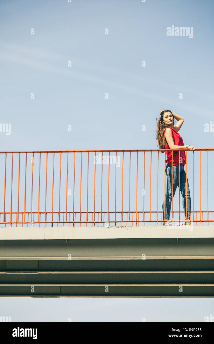 Young long haired girl leaning against railing on a walk the urban ...