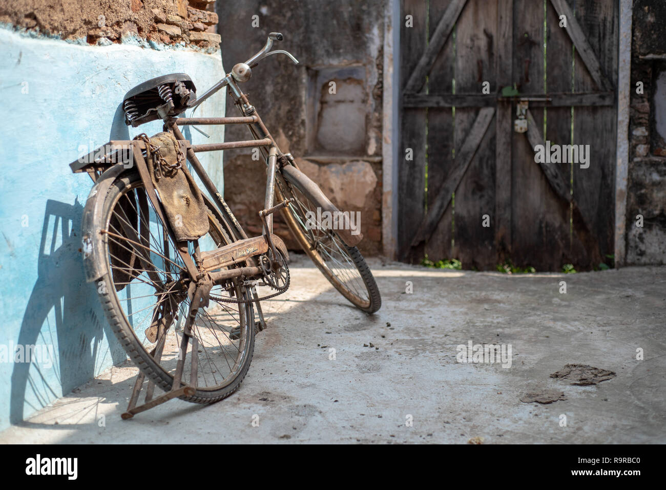 Rusty old bike leaning against a blue wall with shadow. Locked wooden ...