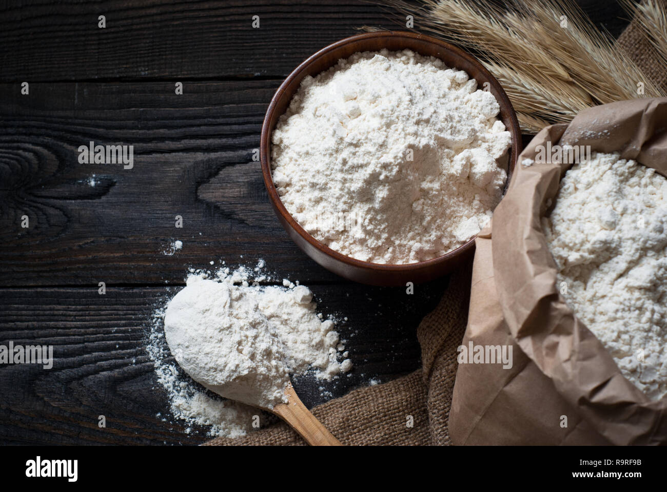 Flour in a wooden bowl, paper bag and spoon. Top view, space for text ...