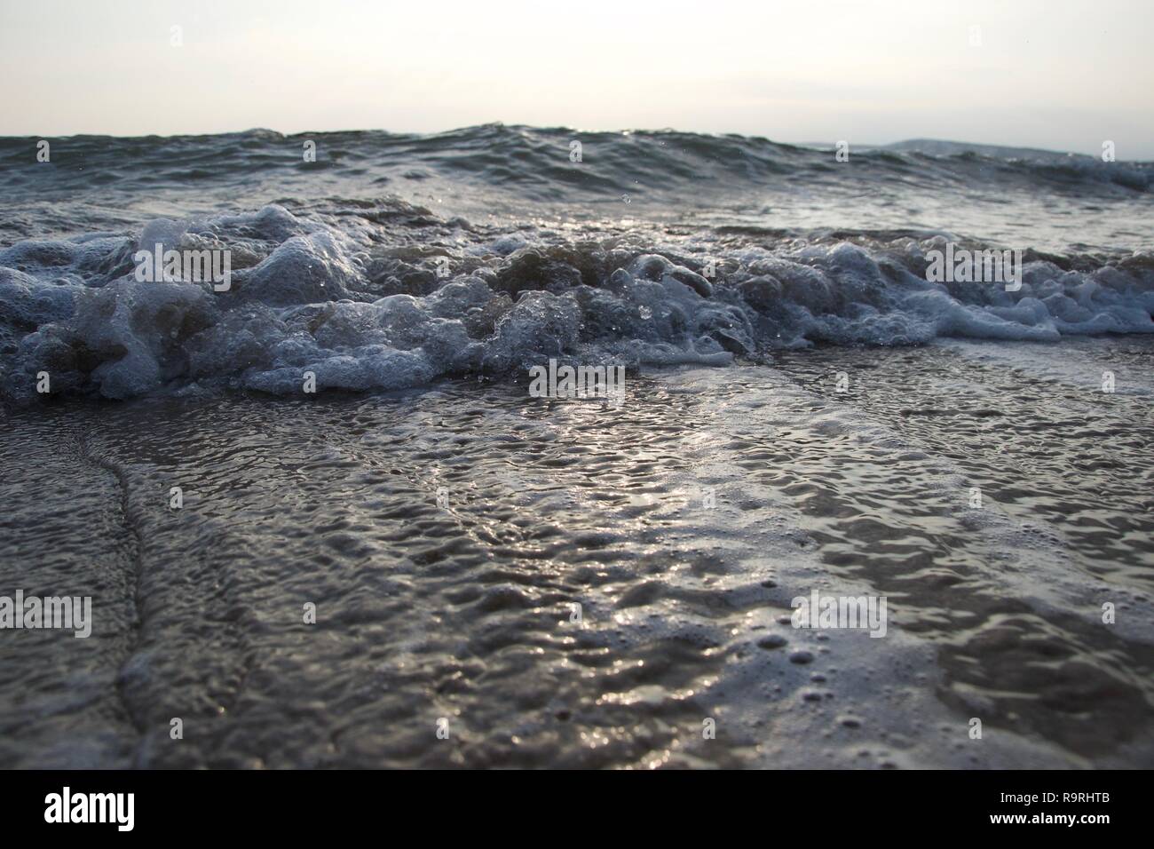 A line of small waves lap a beach as the tide goes out, curling up the ...