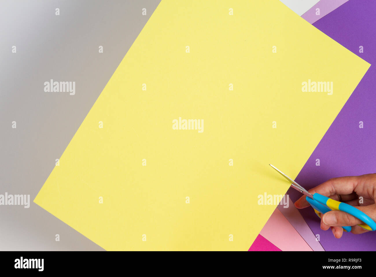 Hand with scissors cutting sheet of yellow color paper Stock Photo - Alamy