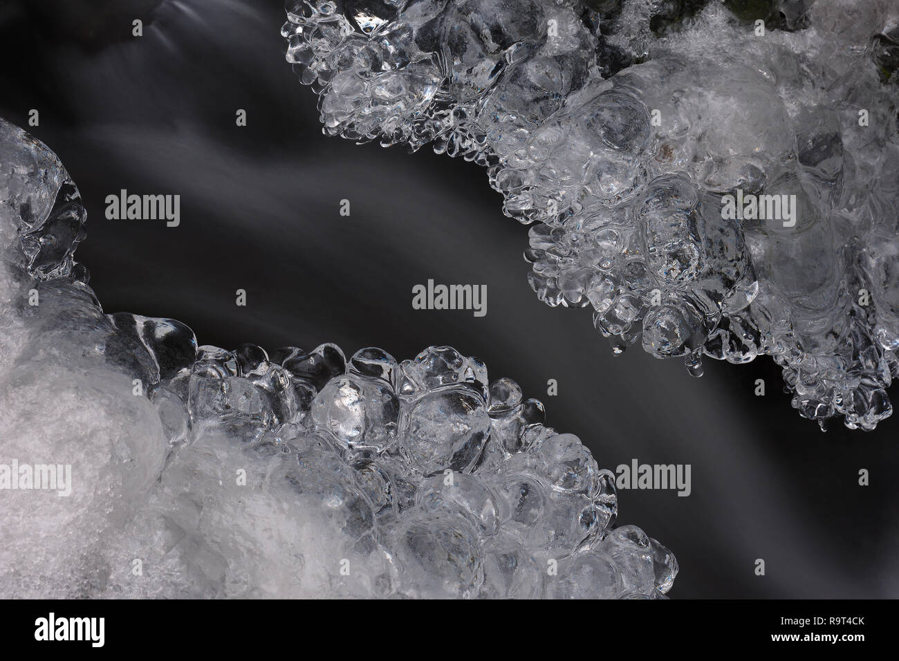 Detail of ice in river. Bright reflections in icicles blur white foam ...