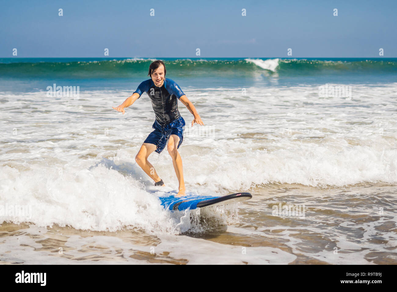 Young man, beginner Surfer learns to surf on a sea foam on the Bali ...