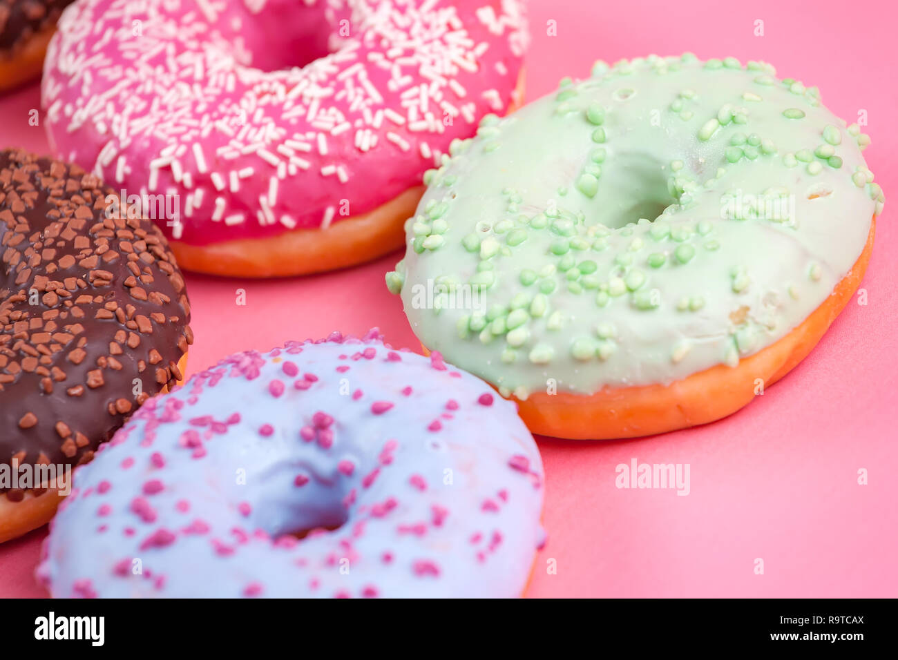 Sweet colorful tasty donuts with icing and sprinkles on pastel pink ...