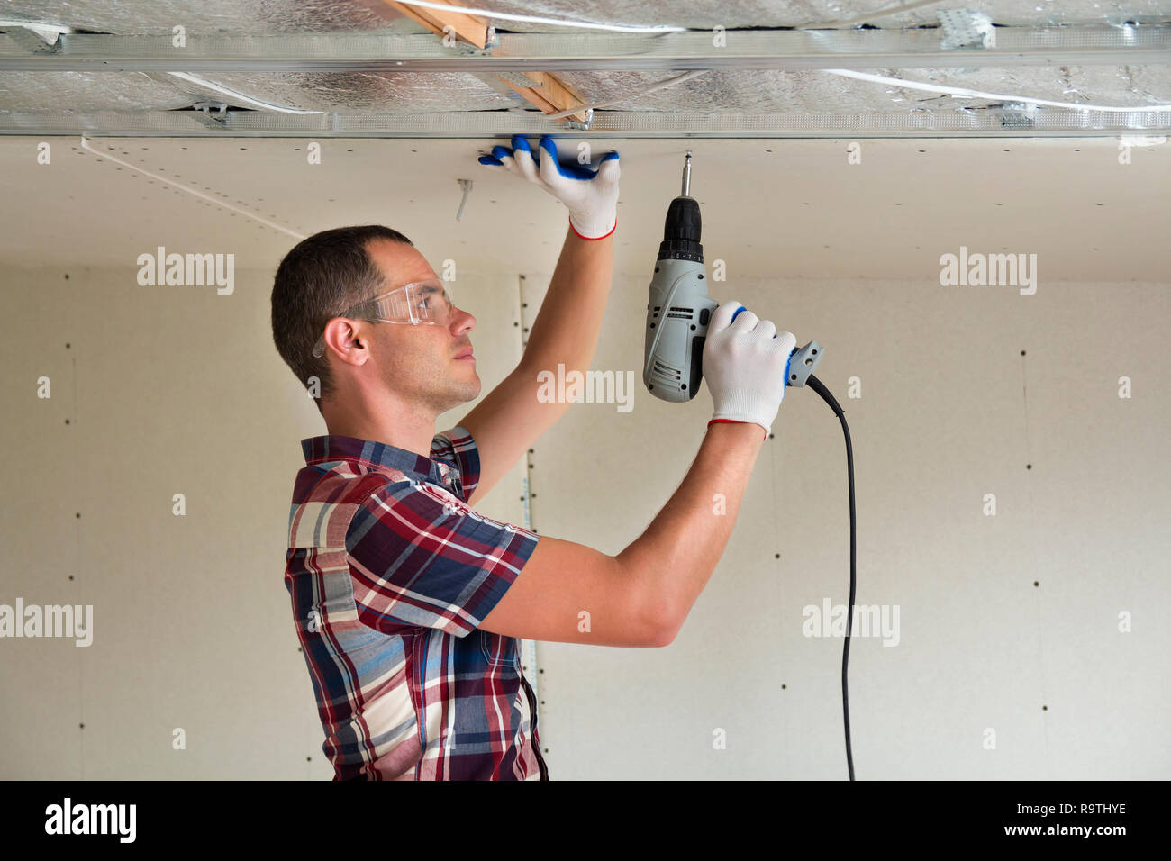 Young man in goggles fixing drywall suspended ceiling to metal frame ...