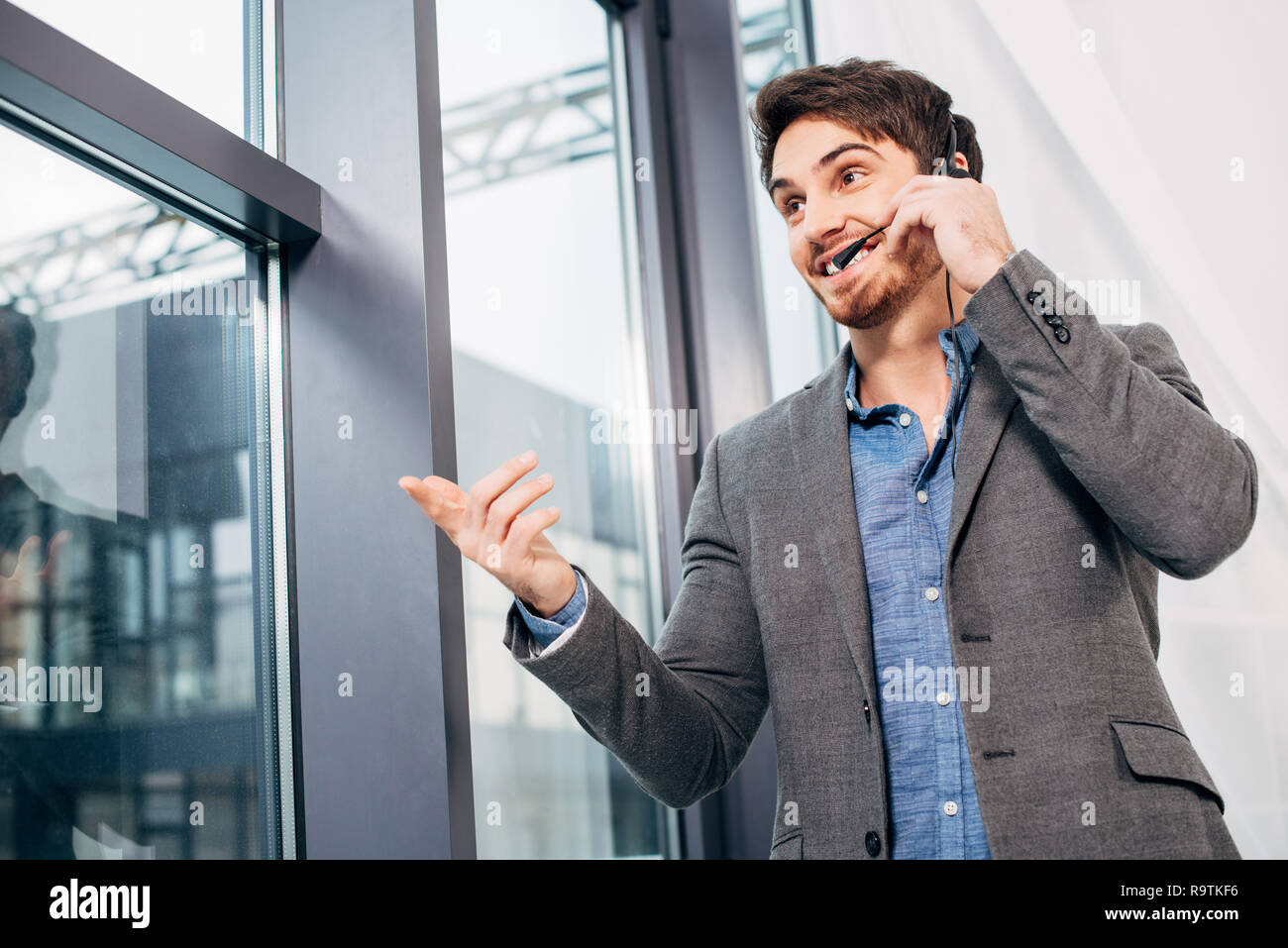 handsome call center operator standing by window, touching headset and ...
