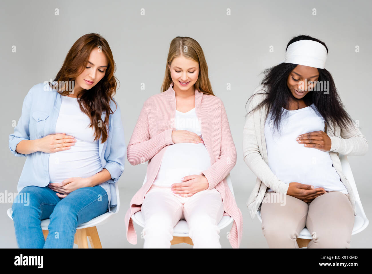 pregnant multiracial women touching bellies and looking down isolated ...
