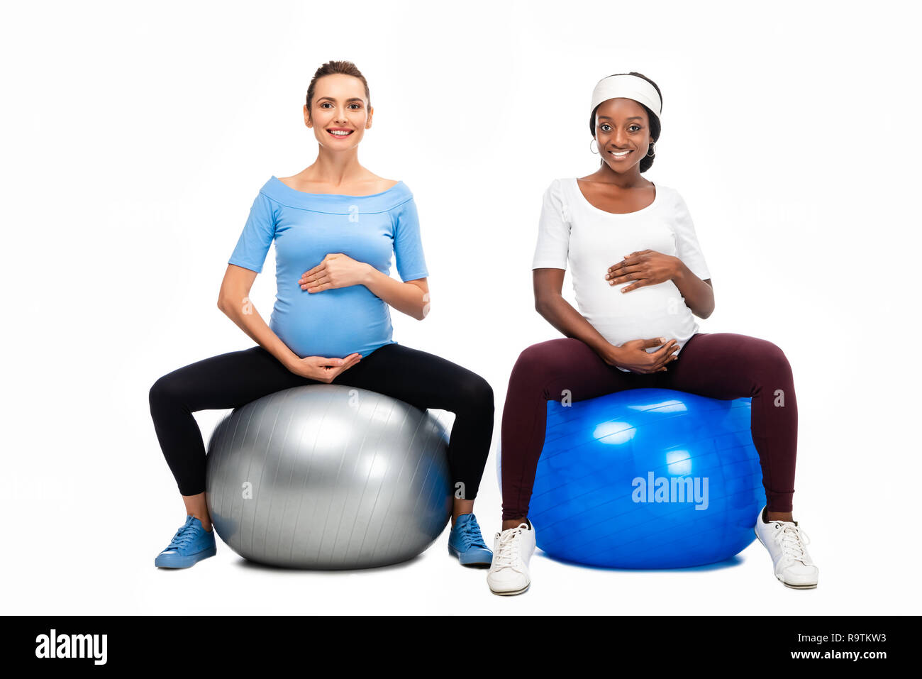 two multicultural pregnant women sitting on fitness balls and holding ...