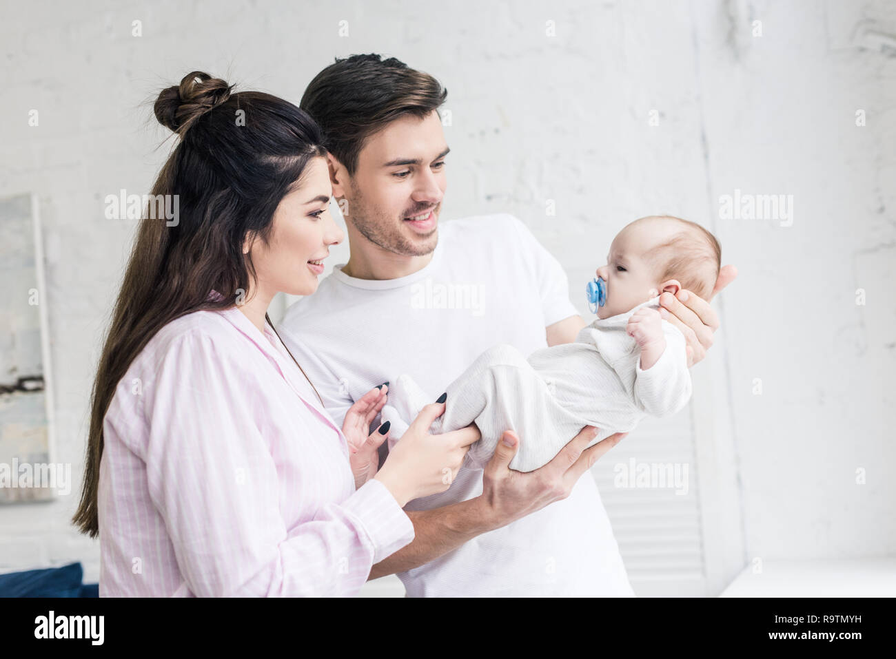 side view of happy parents looking at little son with pacifier at home ...
