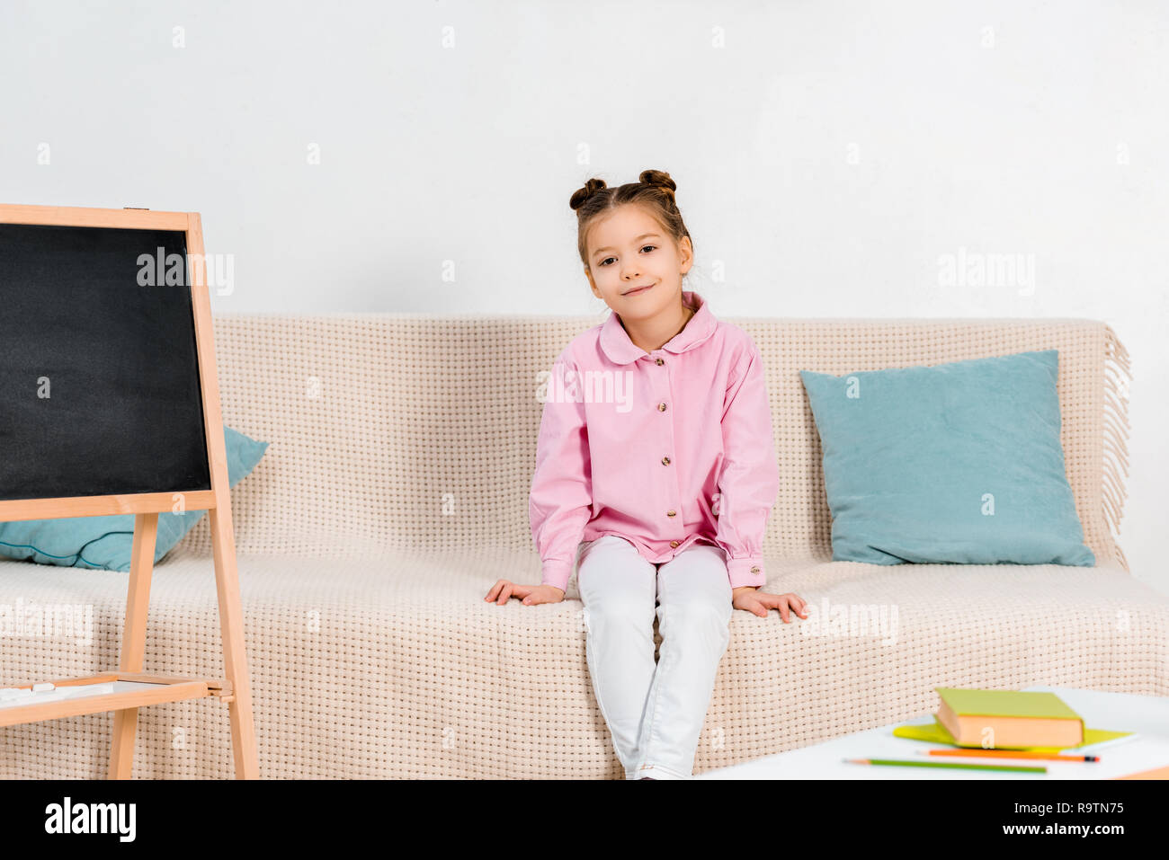 full length view of beautiful little child sitting on couch and smiling ...