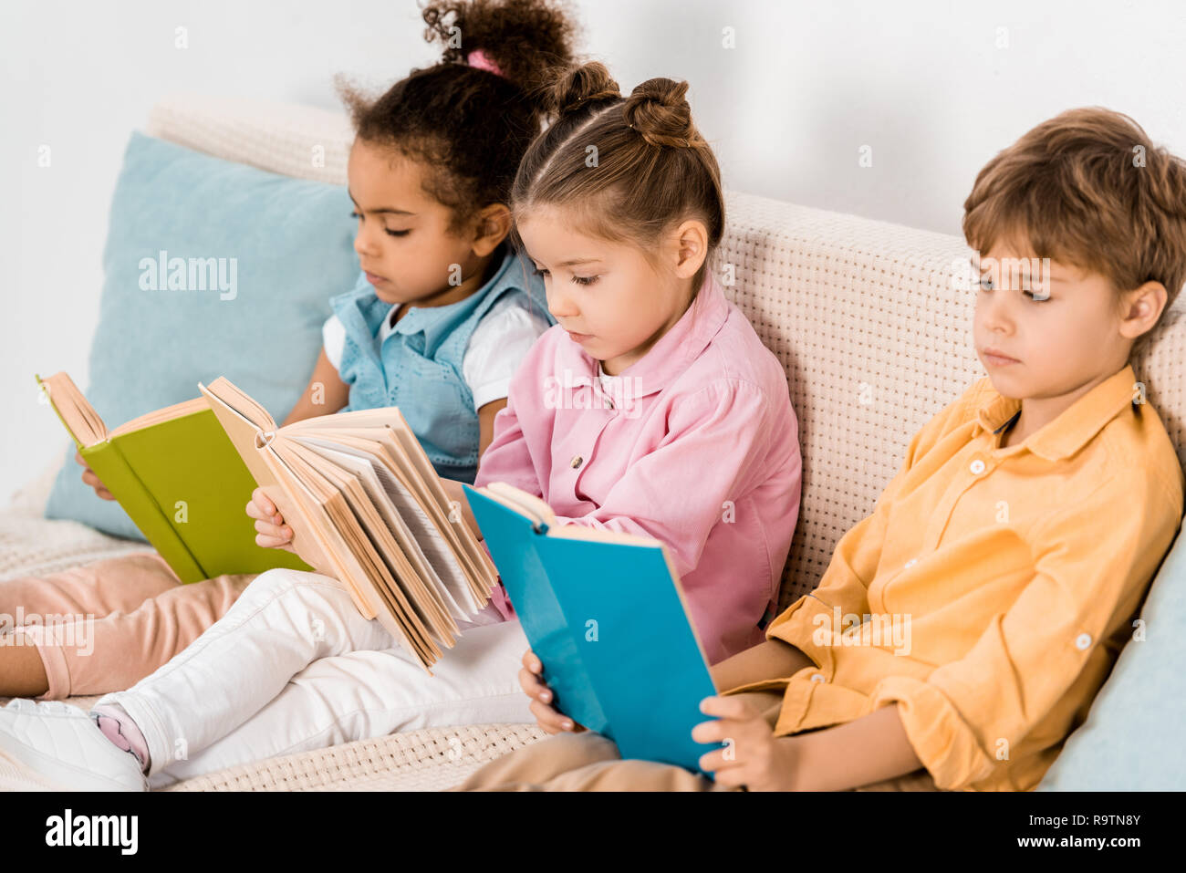 adorable multiethnic children sitting on sofa and reading books Stock ...