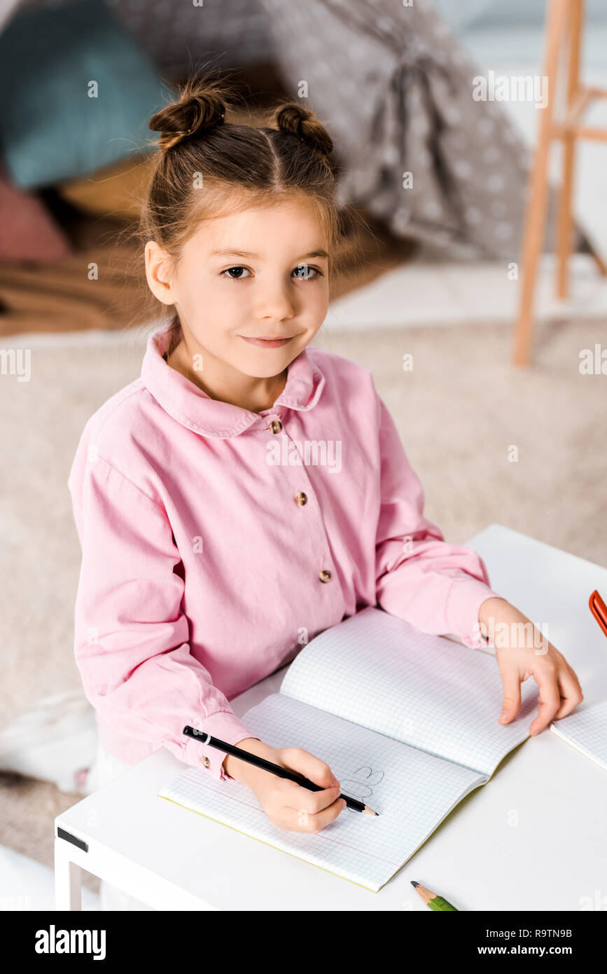 adorable child writing with pencil and smiling at camera Stock Photo ...