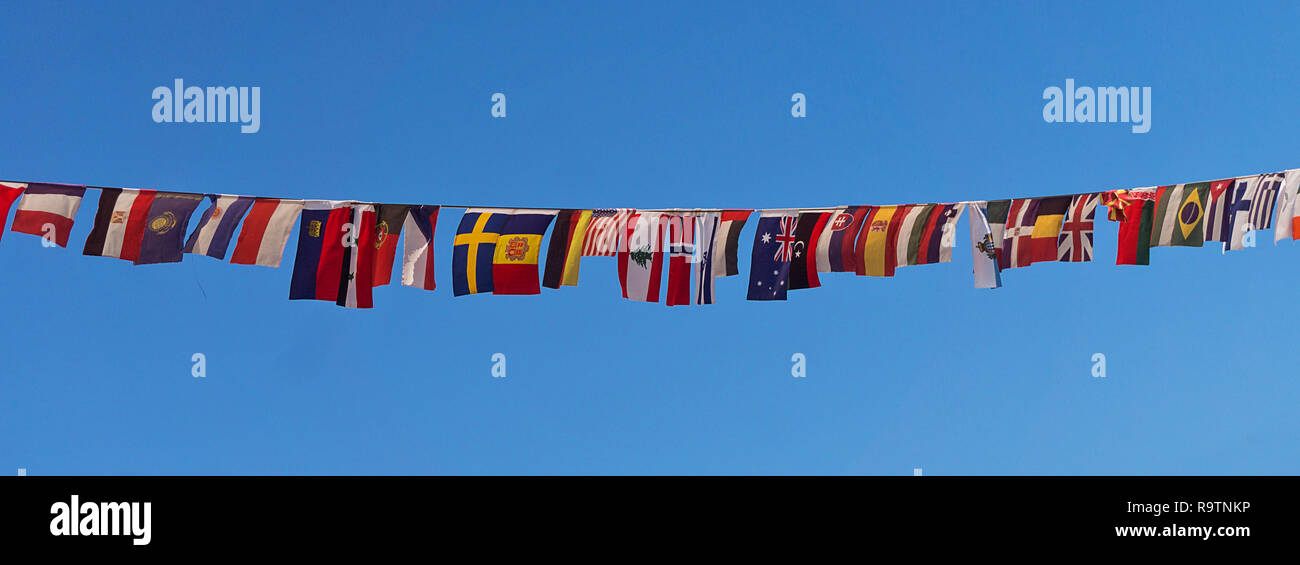 Row of small flags of different countries on a rope against a blue sky ...