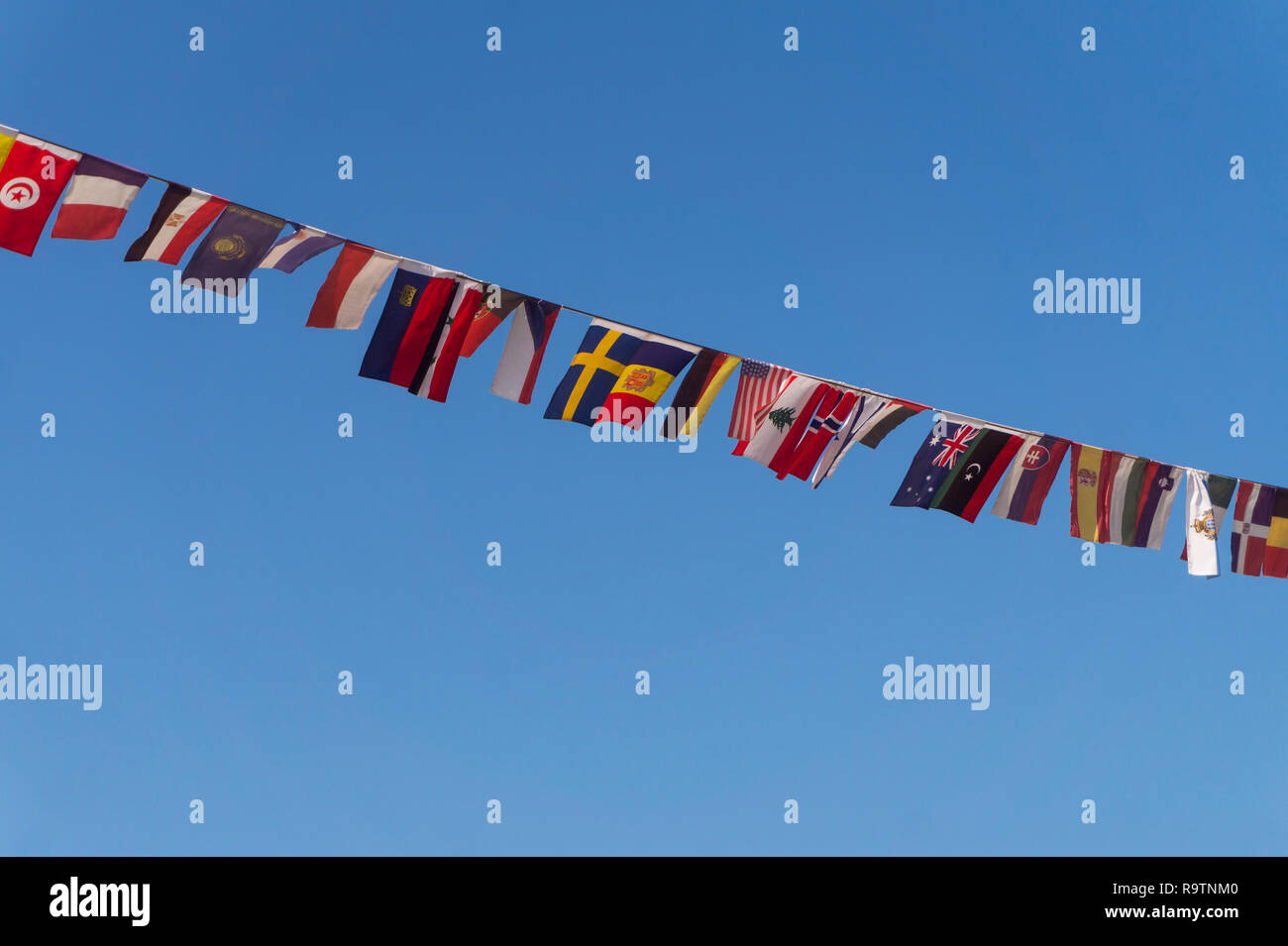 Row of small flags of different countries on a rope against a blue sky ...