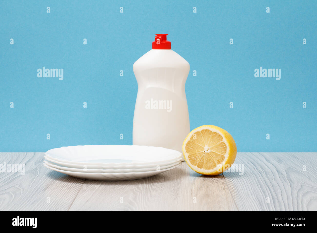 Plastic bottle of dishwashing liquid, clean plates and lemon on wooden ...