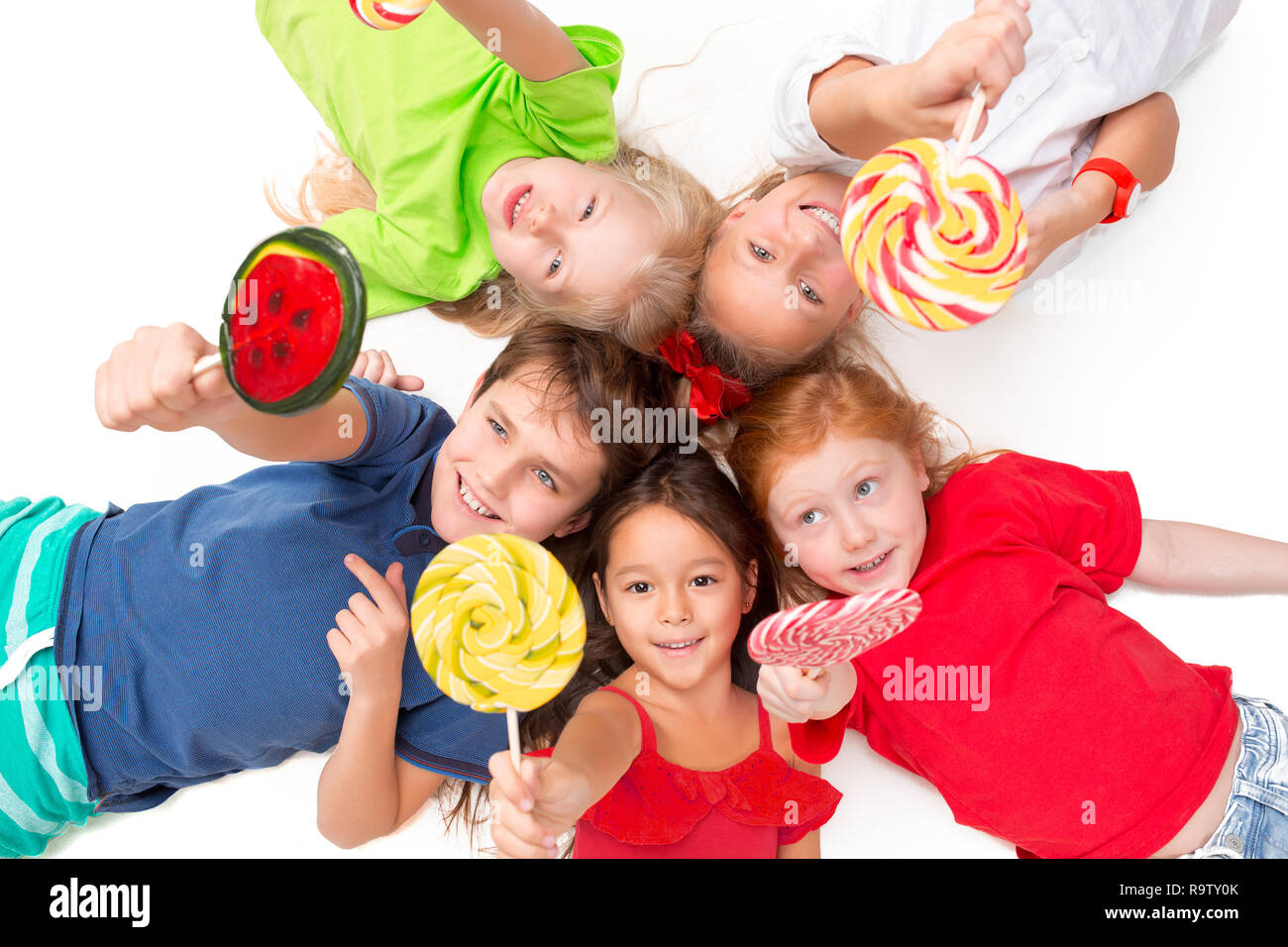 Close-up of happy children with candy lying on floor in studio and ...