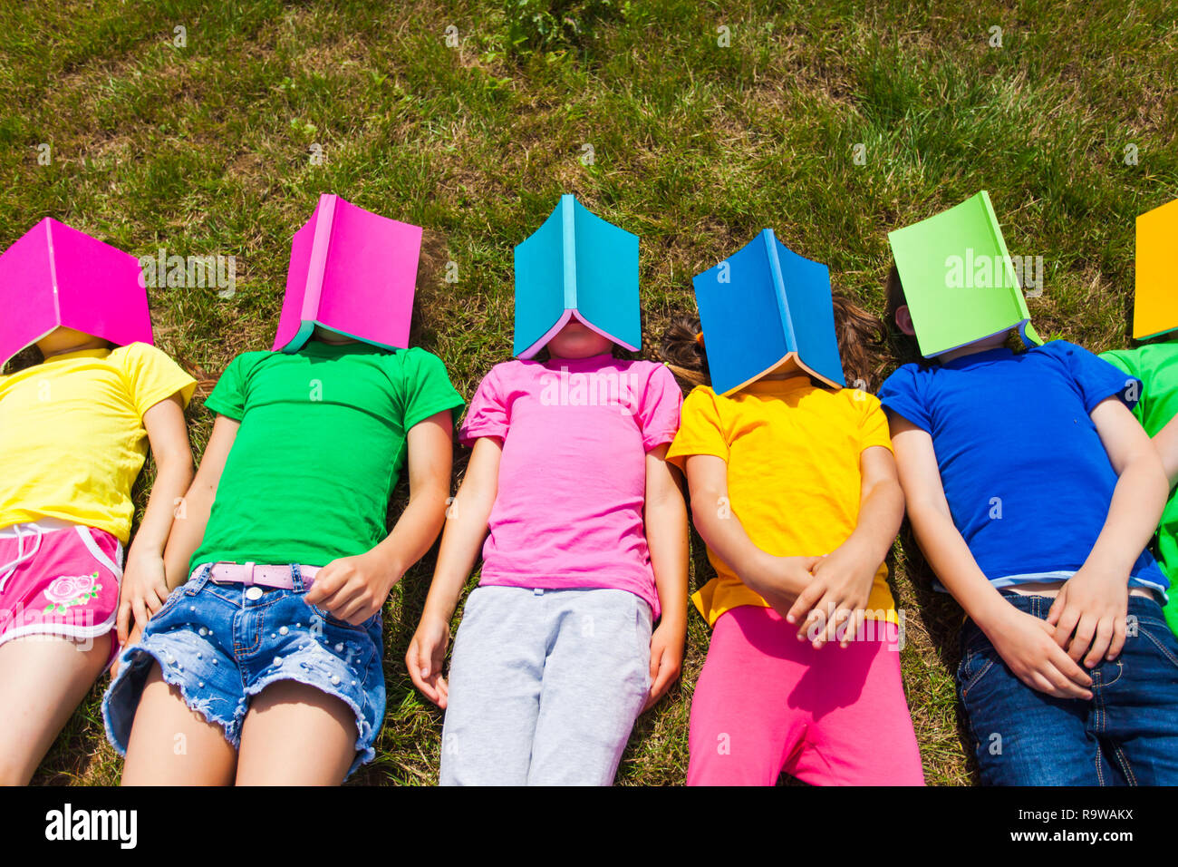 Four kids laying on a ground with books on their faces Stock Photo - Alamy